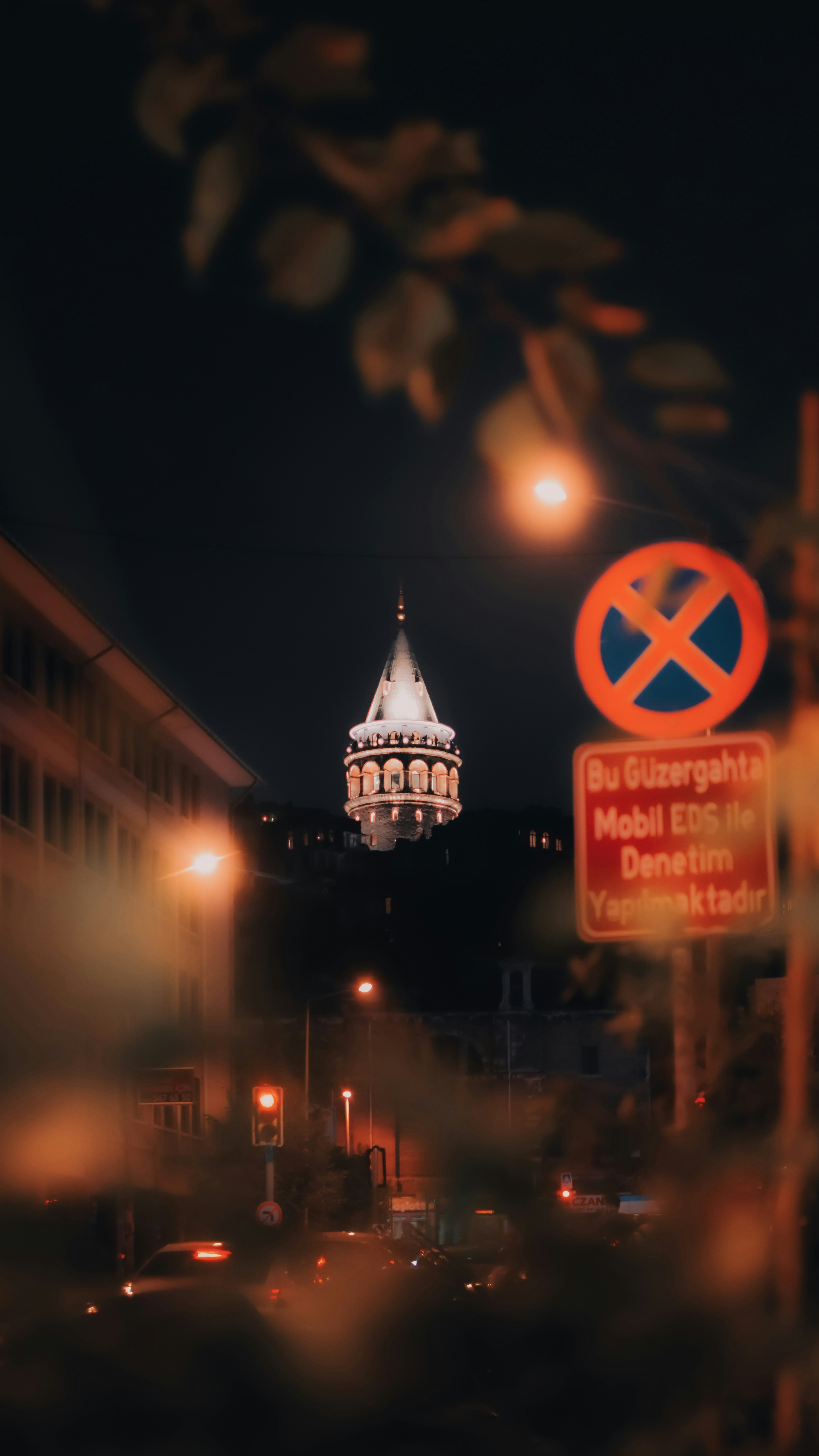 Tall illuminated tower peeks over a blurred urban night street
