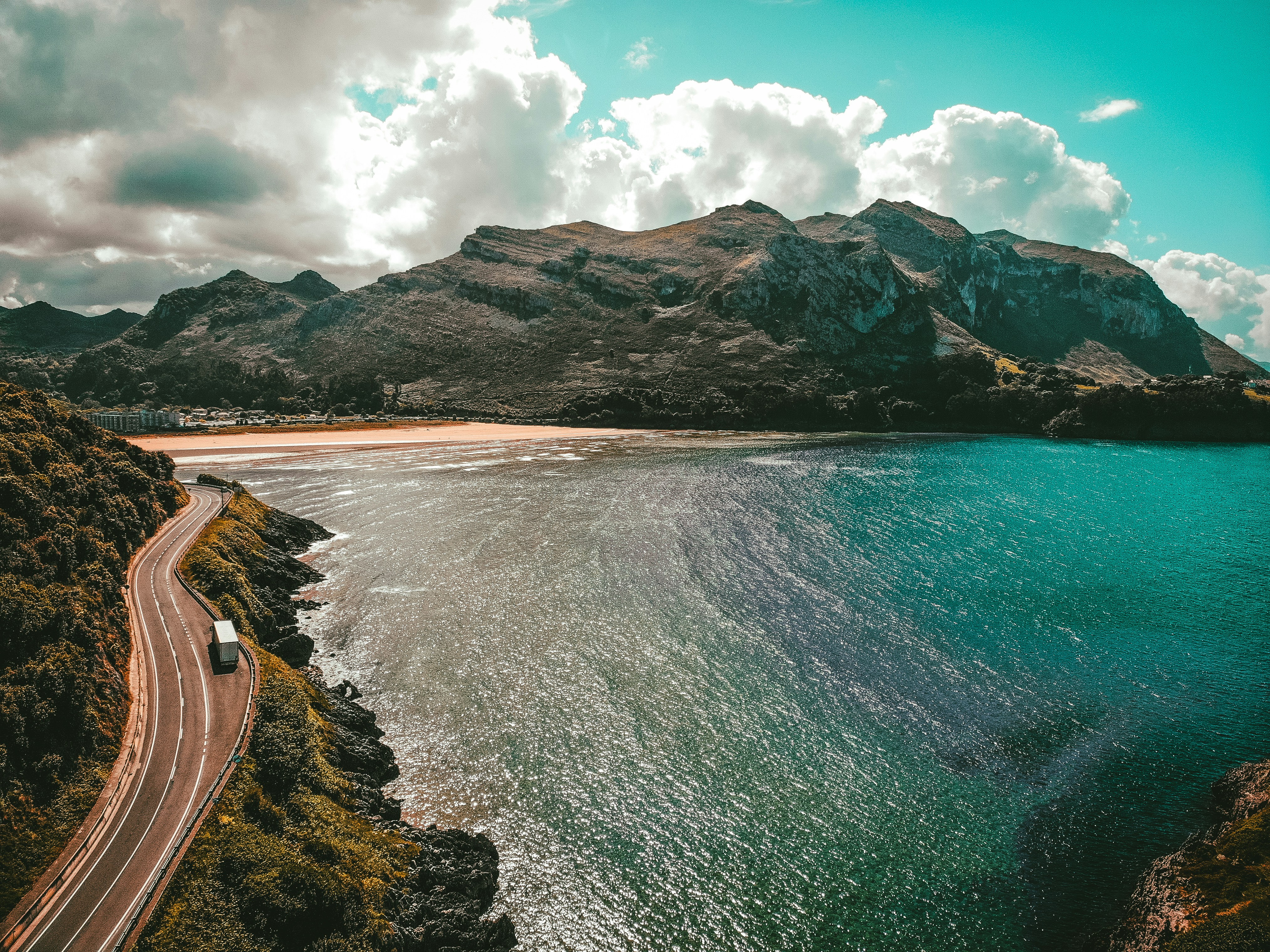 Serpentine Seascape: Coast Road Winding Along Turquoise Waters Under Looming Peaks