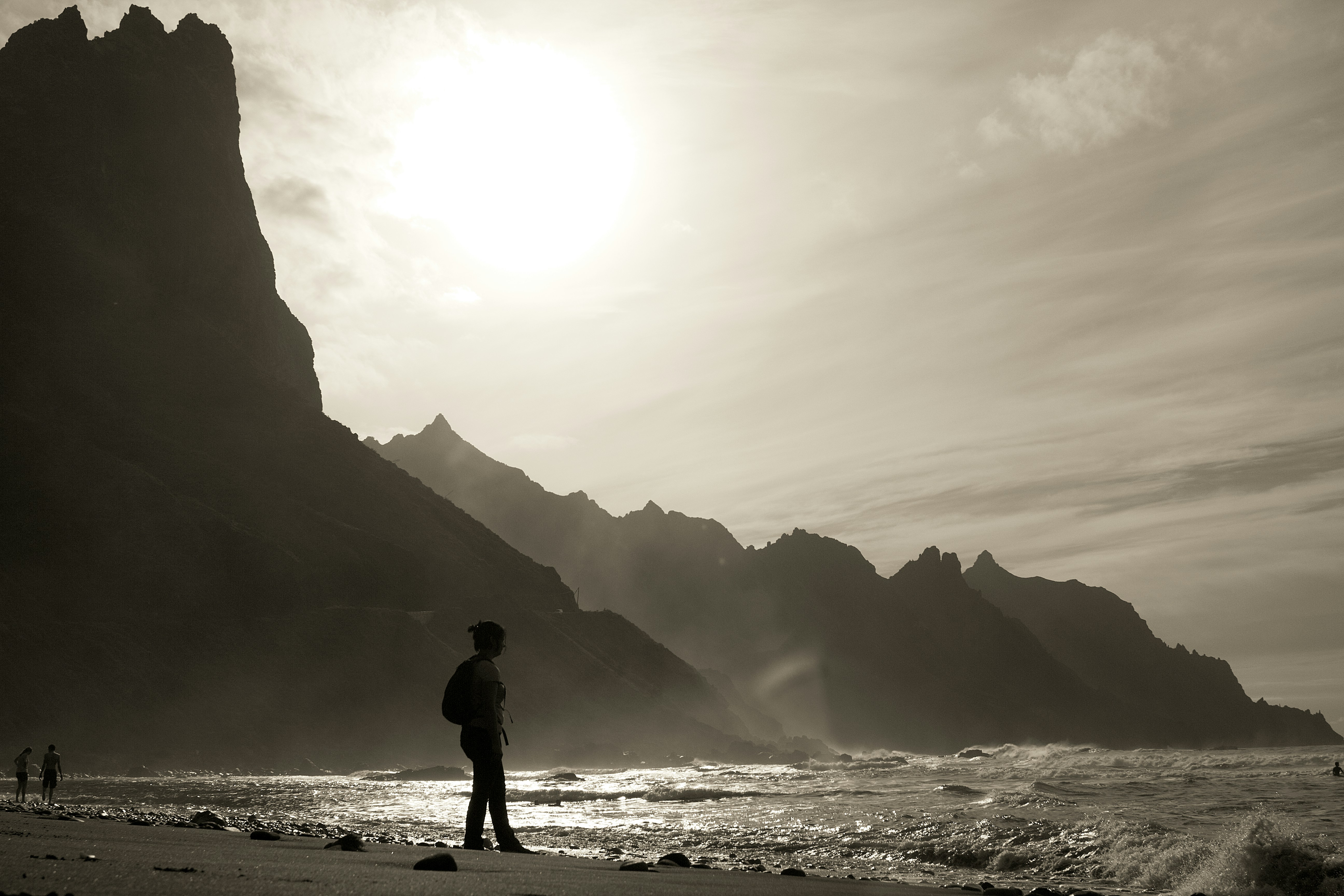 Lone Silhouette on a Rugged Sepia Coastline Beneath a Looming Sun