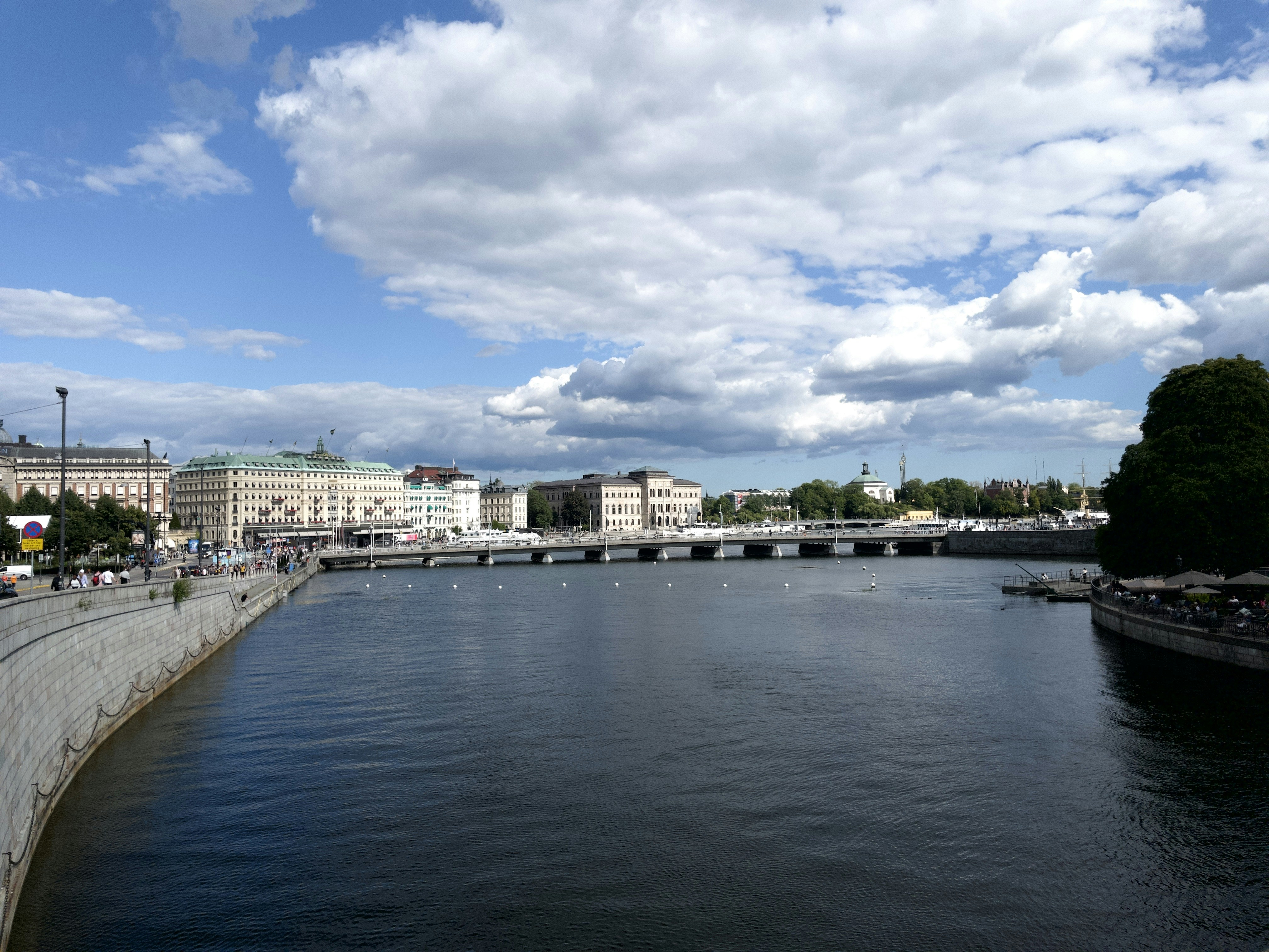 Pastel Promenade: A Sunlit European Riverfront Under a Cloud-Sculpted Sky