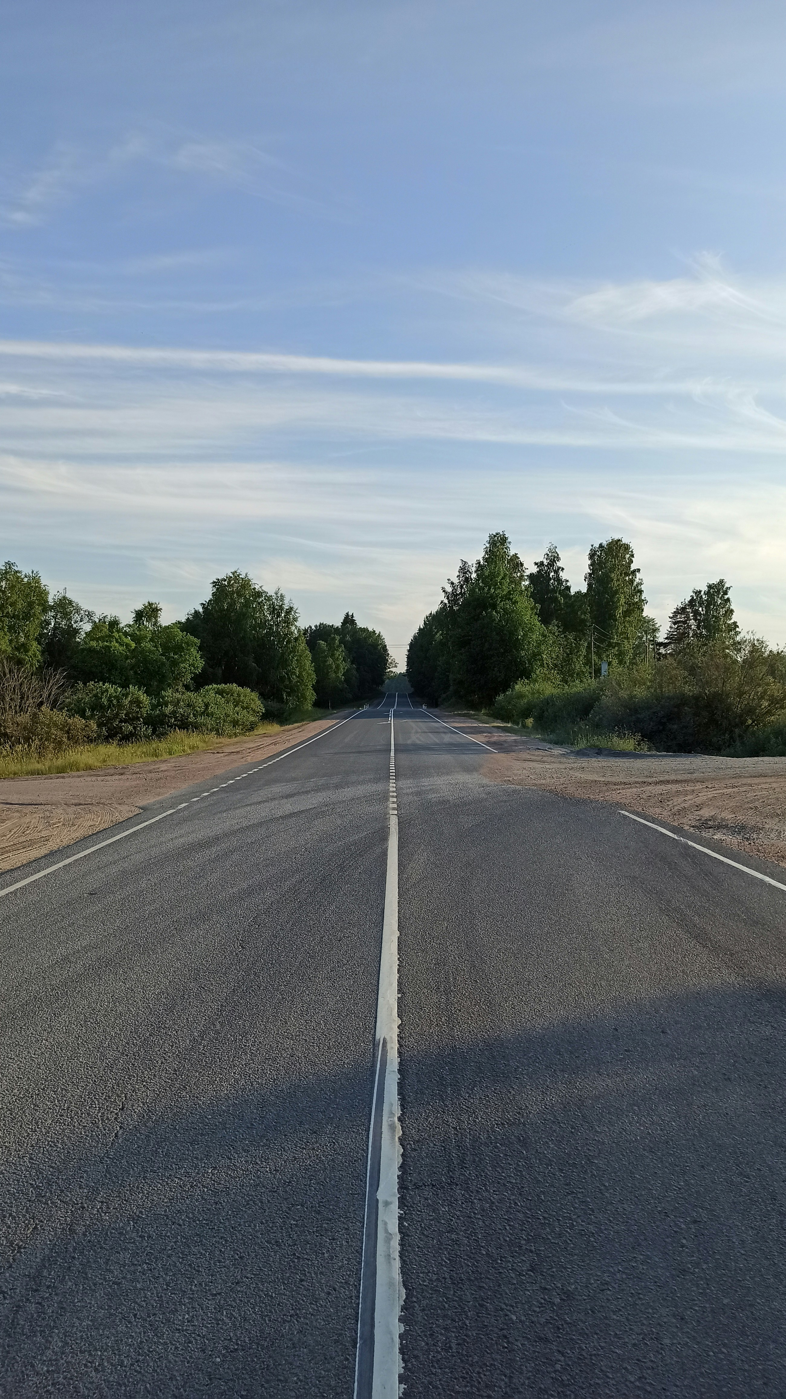 A long, straight road flanked by lush greenery under a clear sky, inviting exploration and tranquility.
