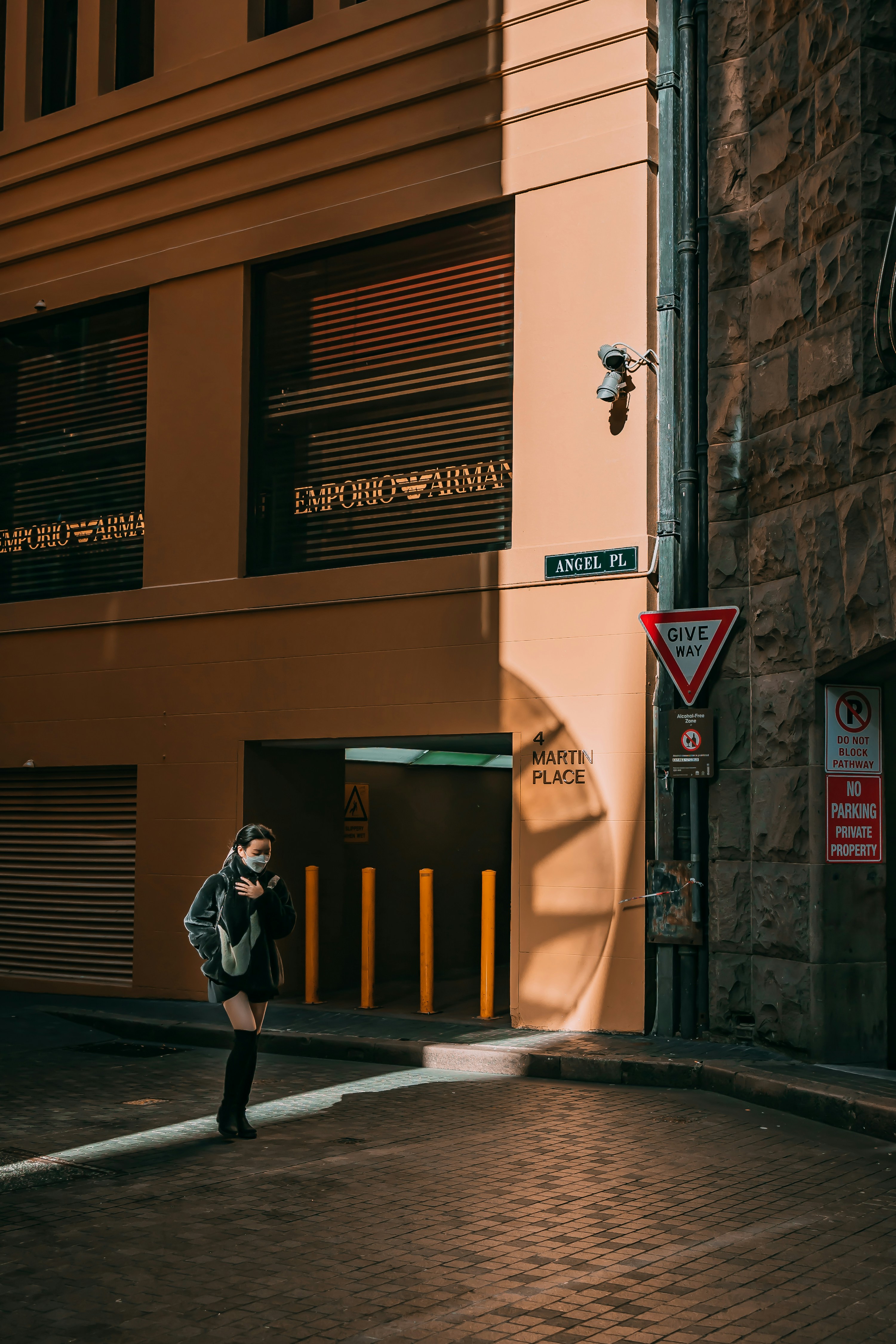 Sunlit stride under peach walls: a masked pedestrian in urban light