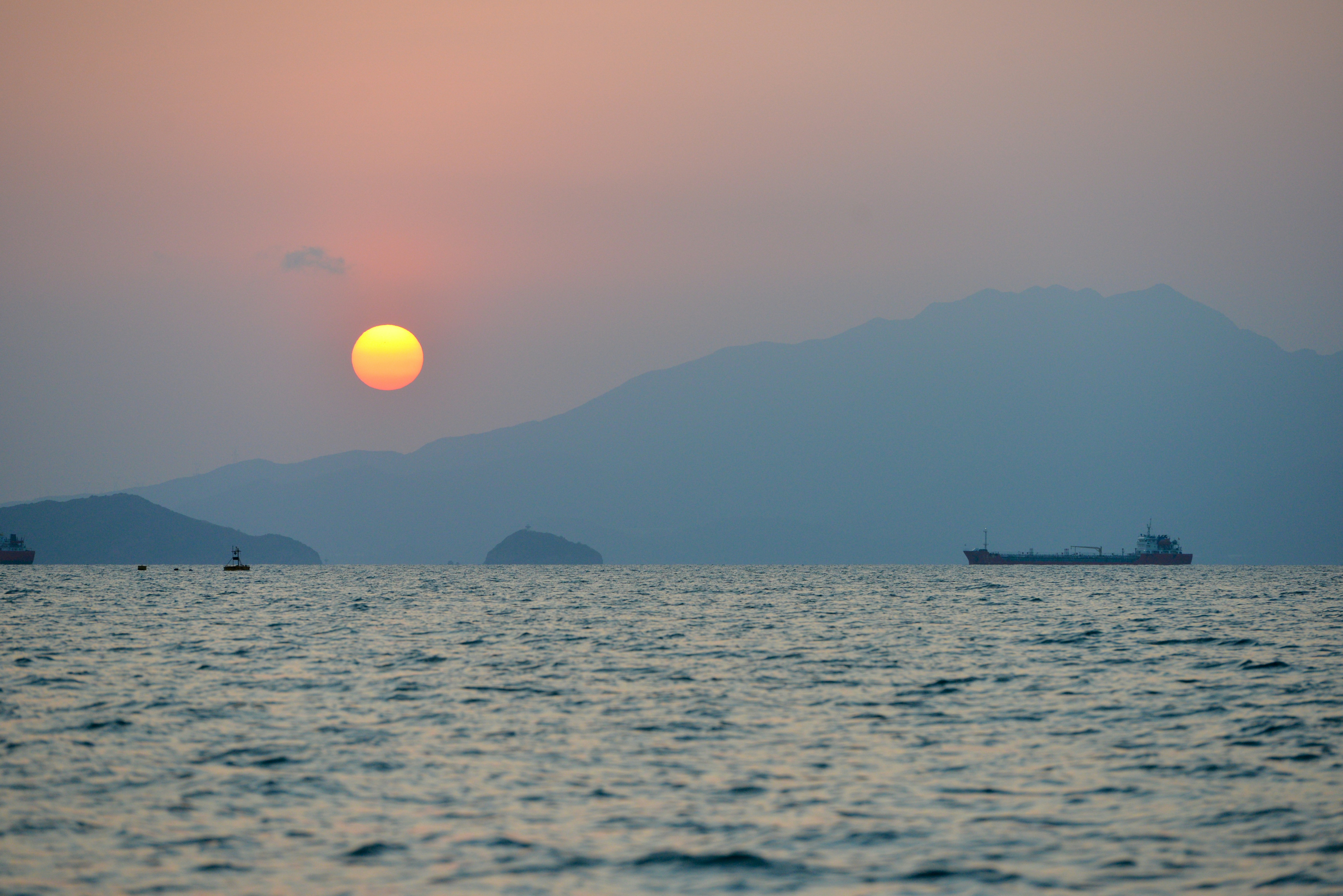 Sun setting over a tranquil sea with misty mountains in the background.