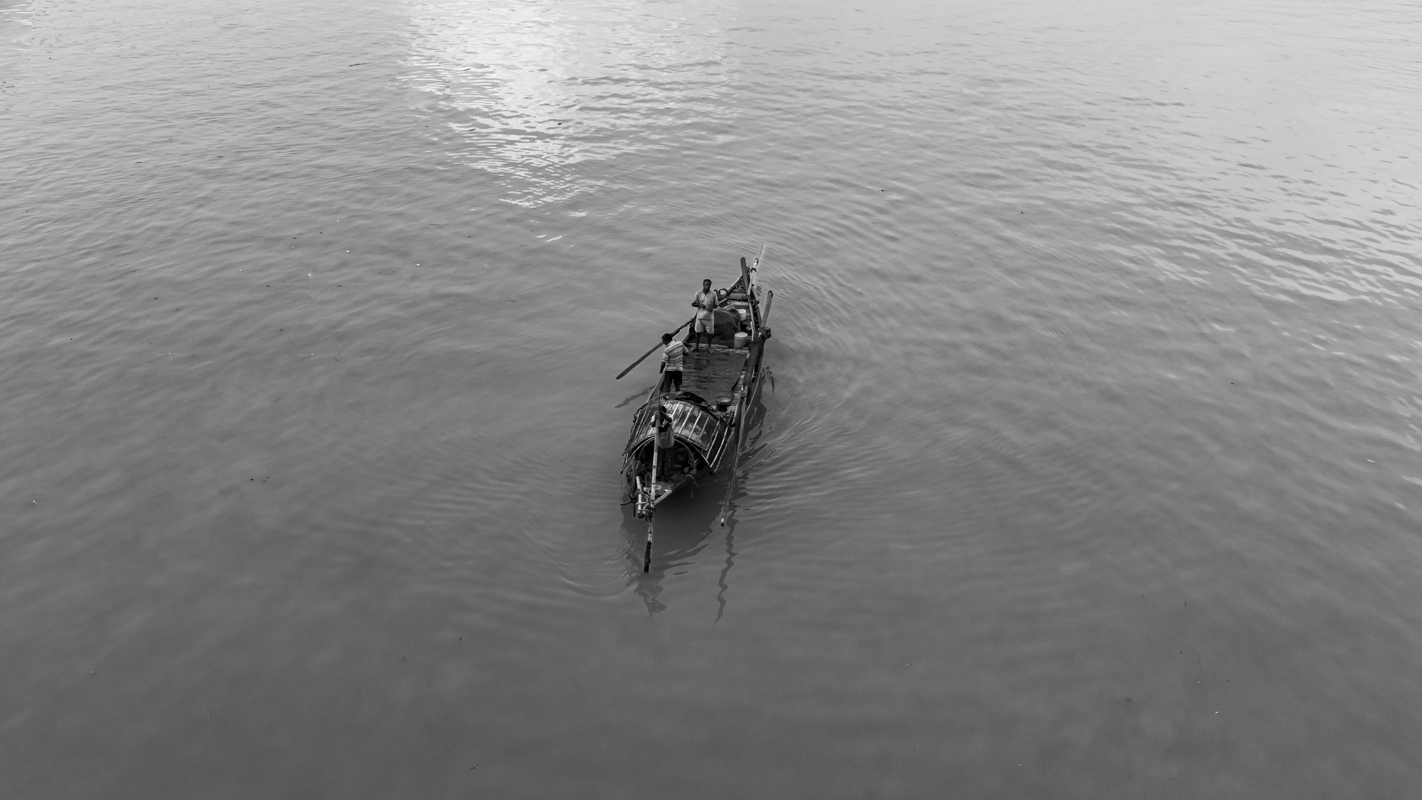 A small boat with two men rows across the calm waters of the Ganges River, captured in serene black and white.