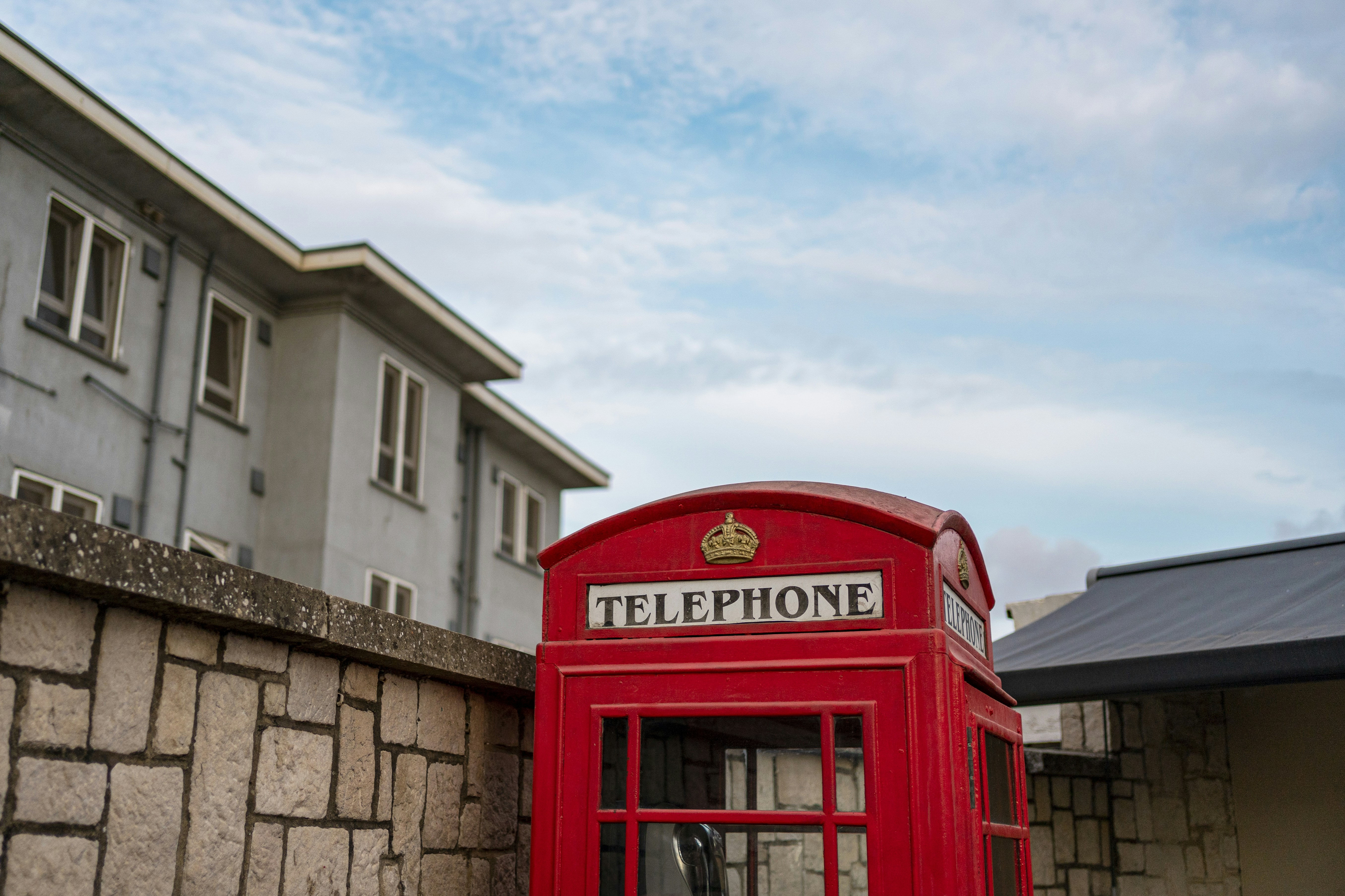 Crimson Telephone Booth Standing Guard beside a Weathered Stone Wall Under a Clear Sky