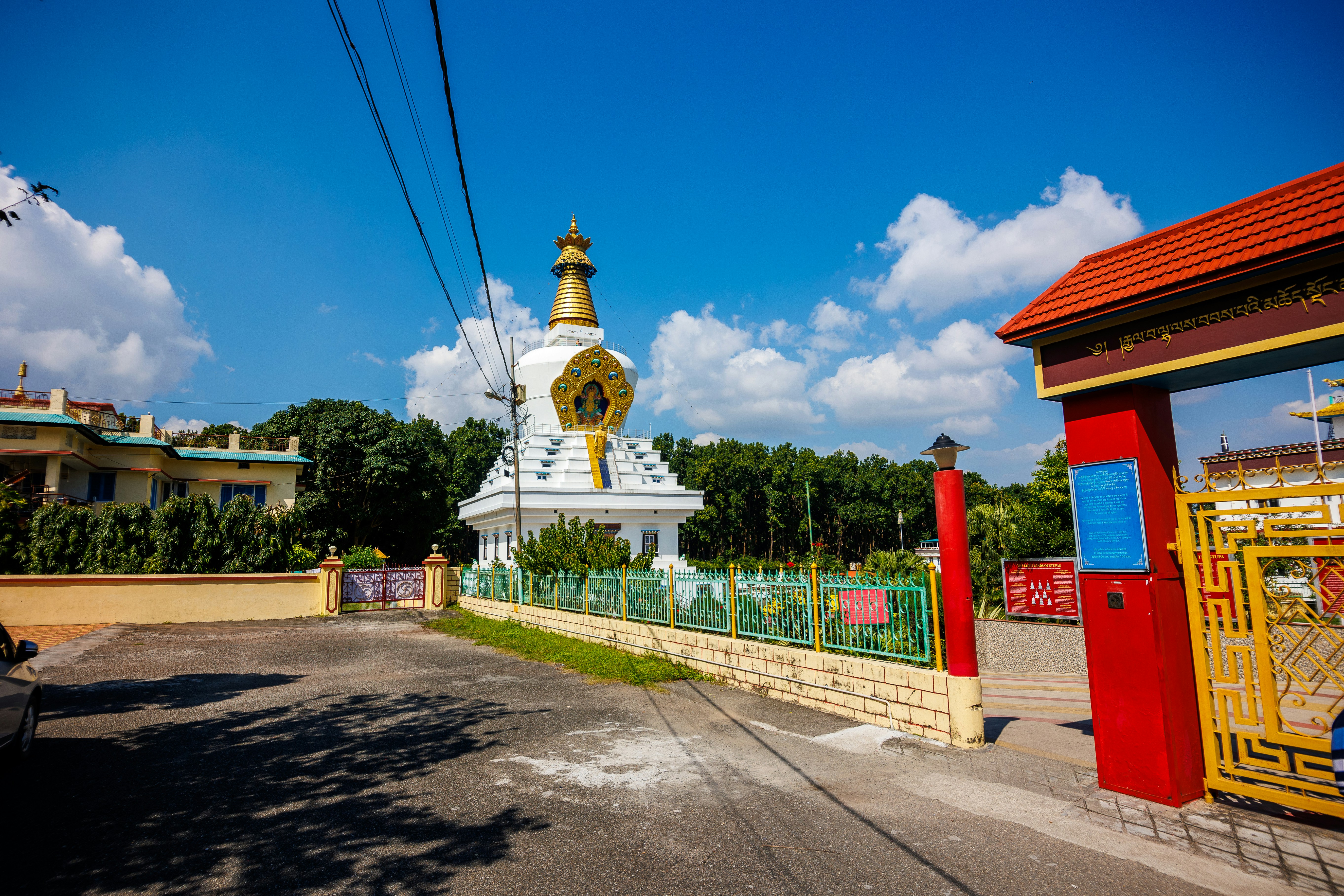 White stupa under a bright blue sky with surrounding greenery and traditional architecture.