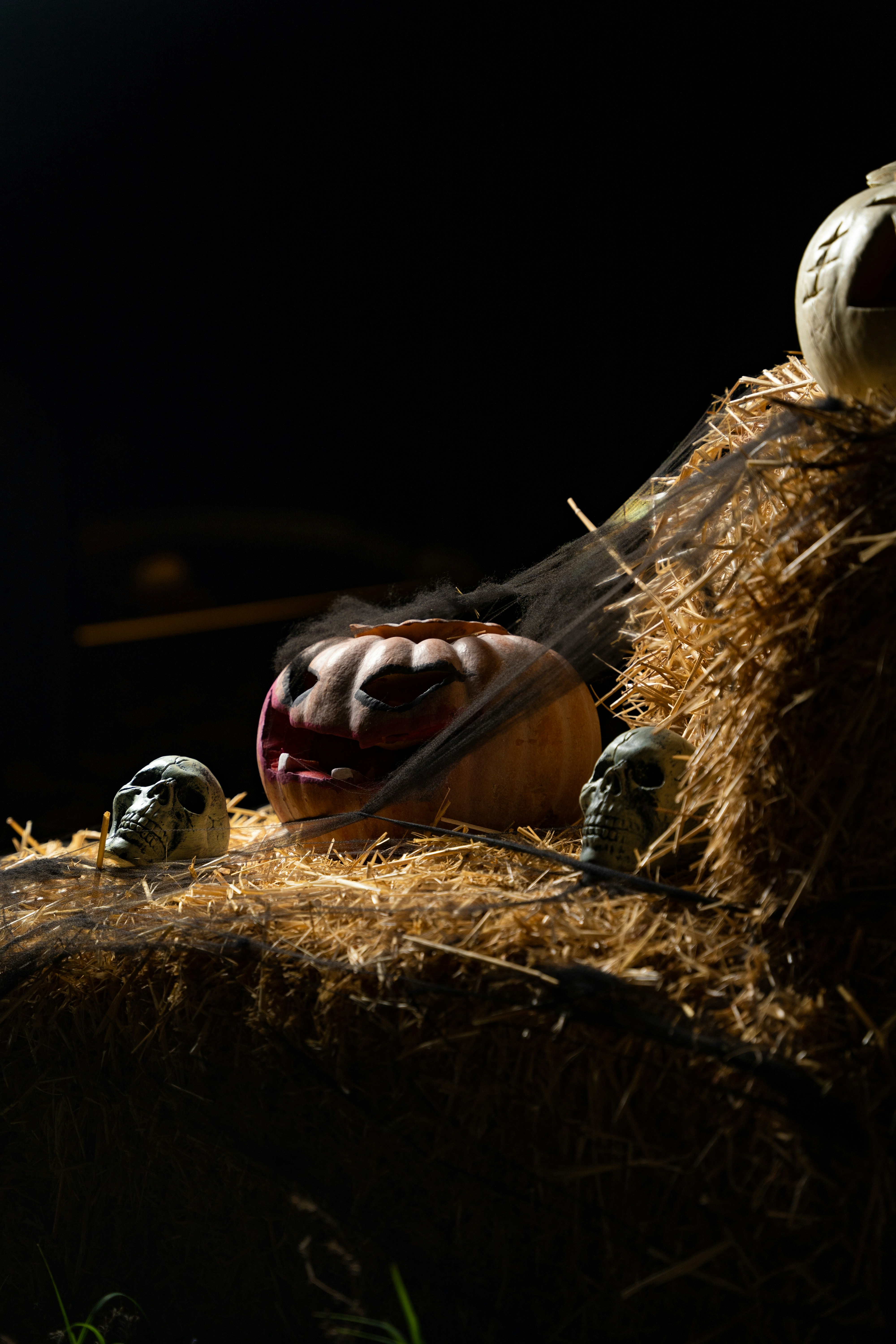 Grin in the Hay: A Carved Pumpkin Surrounded by Cobwebs and Skull Accents