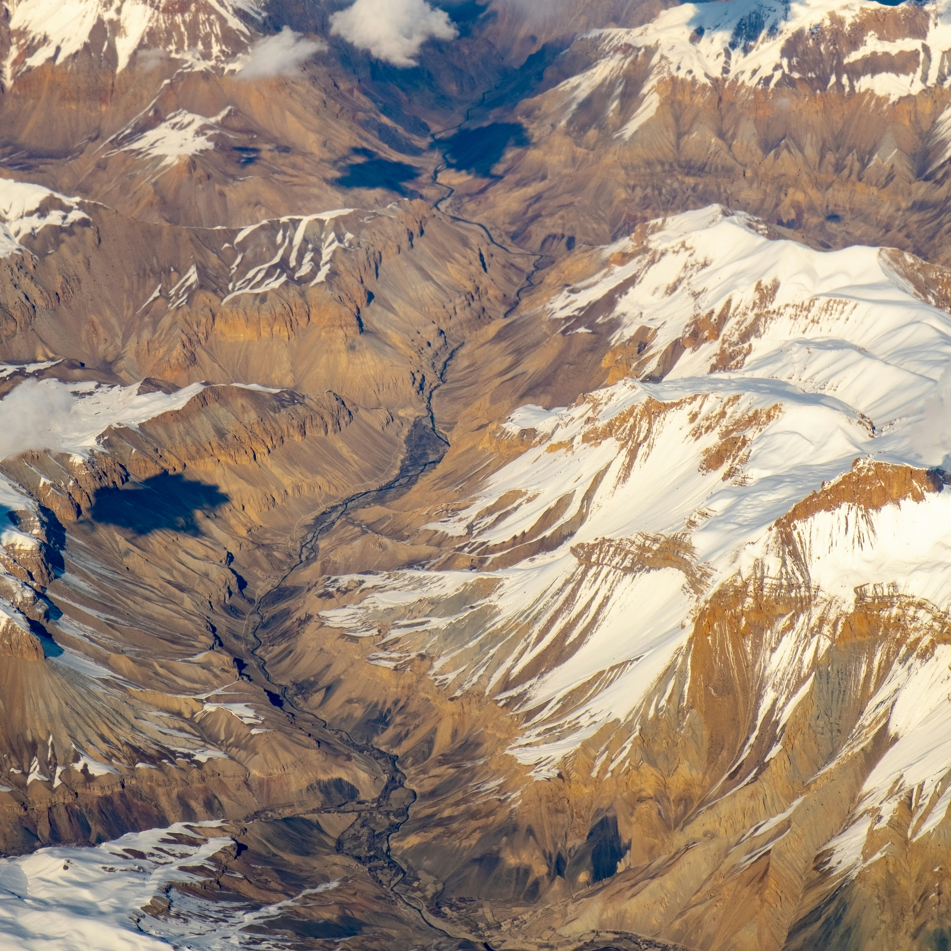 Aerial view of rugged mountain terrain, showcasing snow-capped peaks and intricate valleys. The interplay of light and shadow highlights the natural contours.