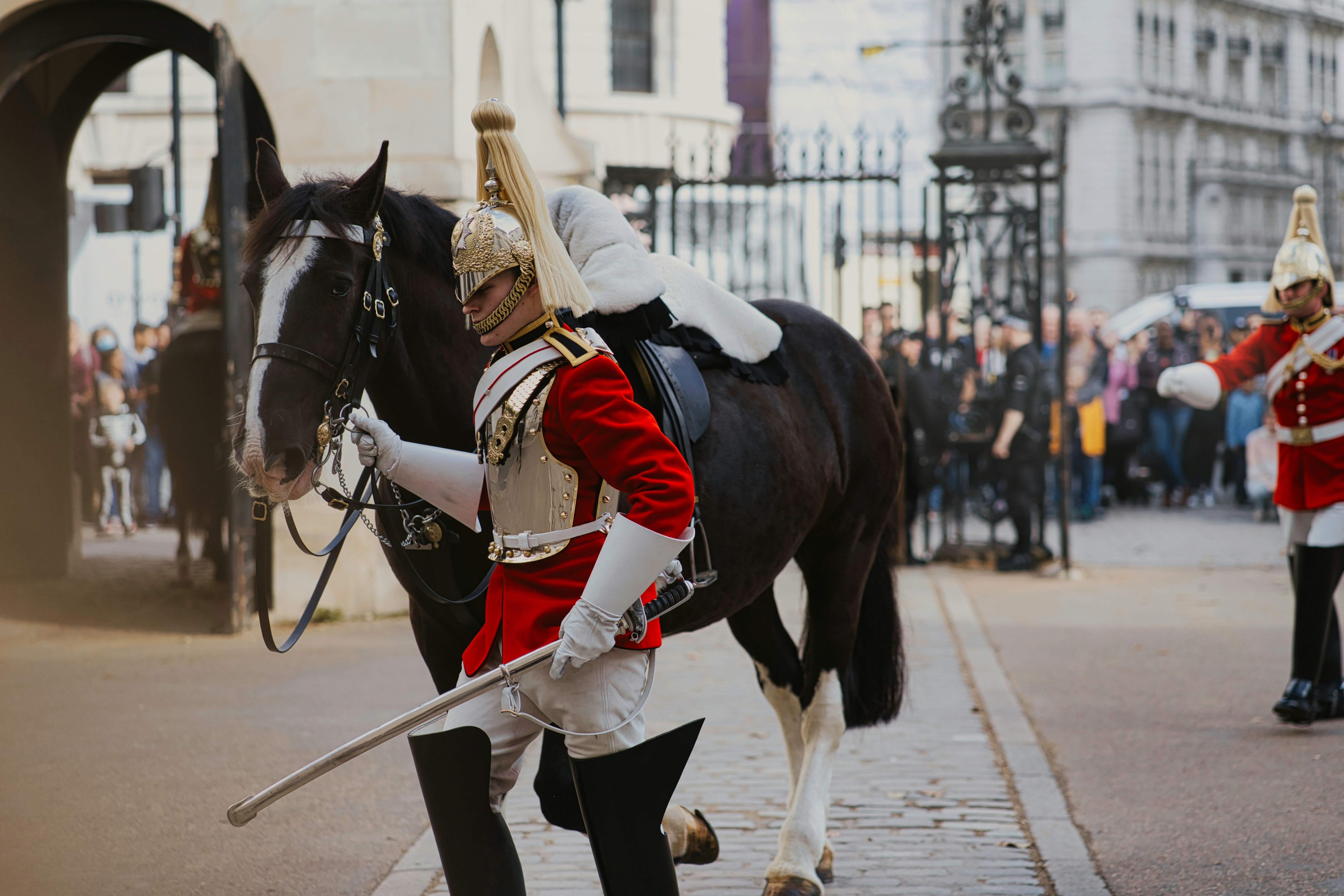 Guards in traditional red uniforms lead horses through a historic courtyard during a formal parade.