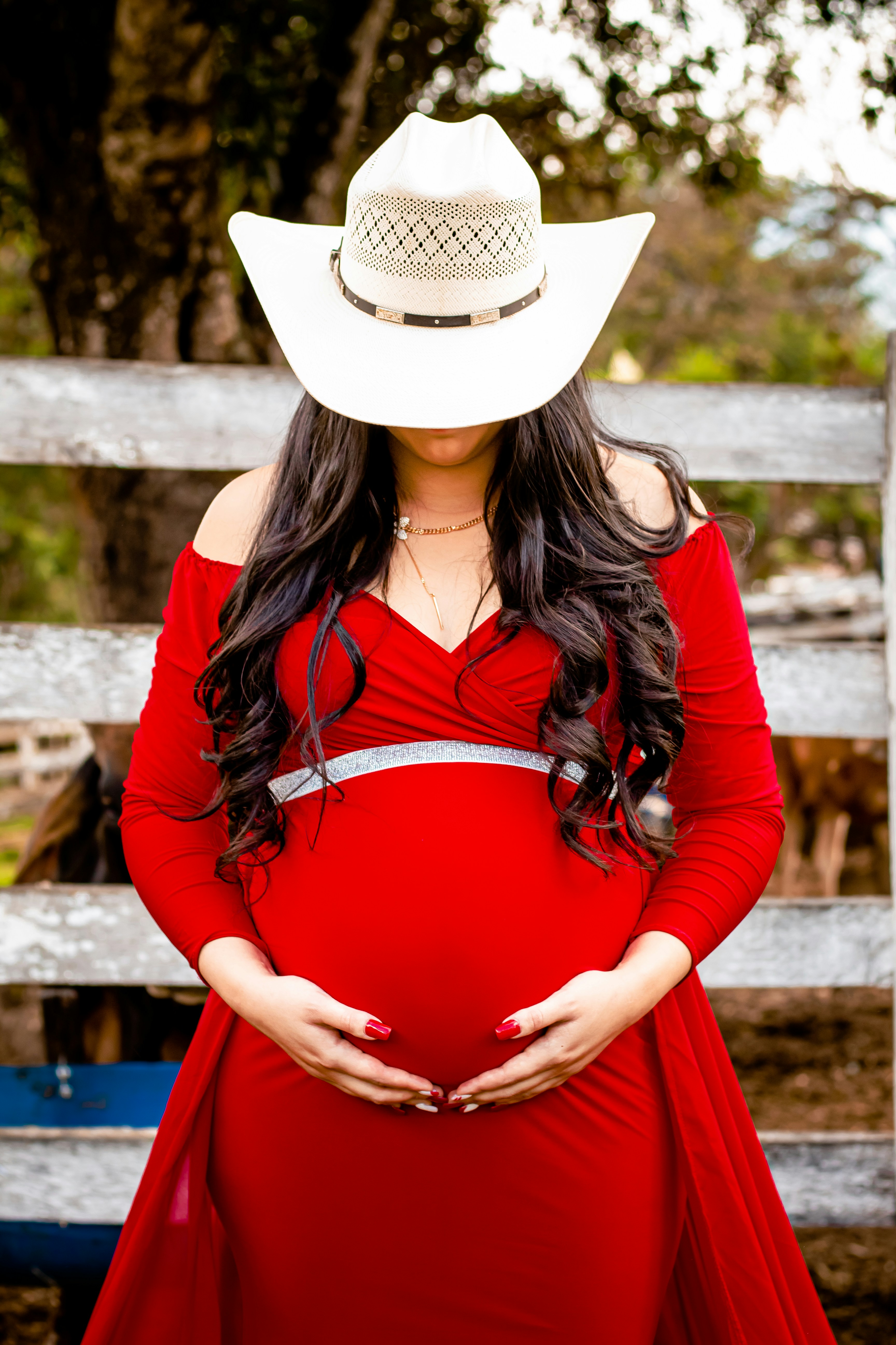Crimson Glow: A Pregnant Portrait Beneath a Cowboy Hat in Rustic Light