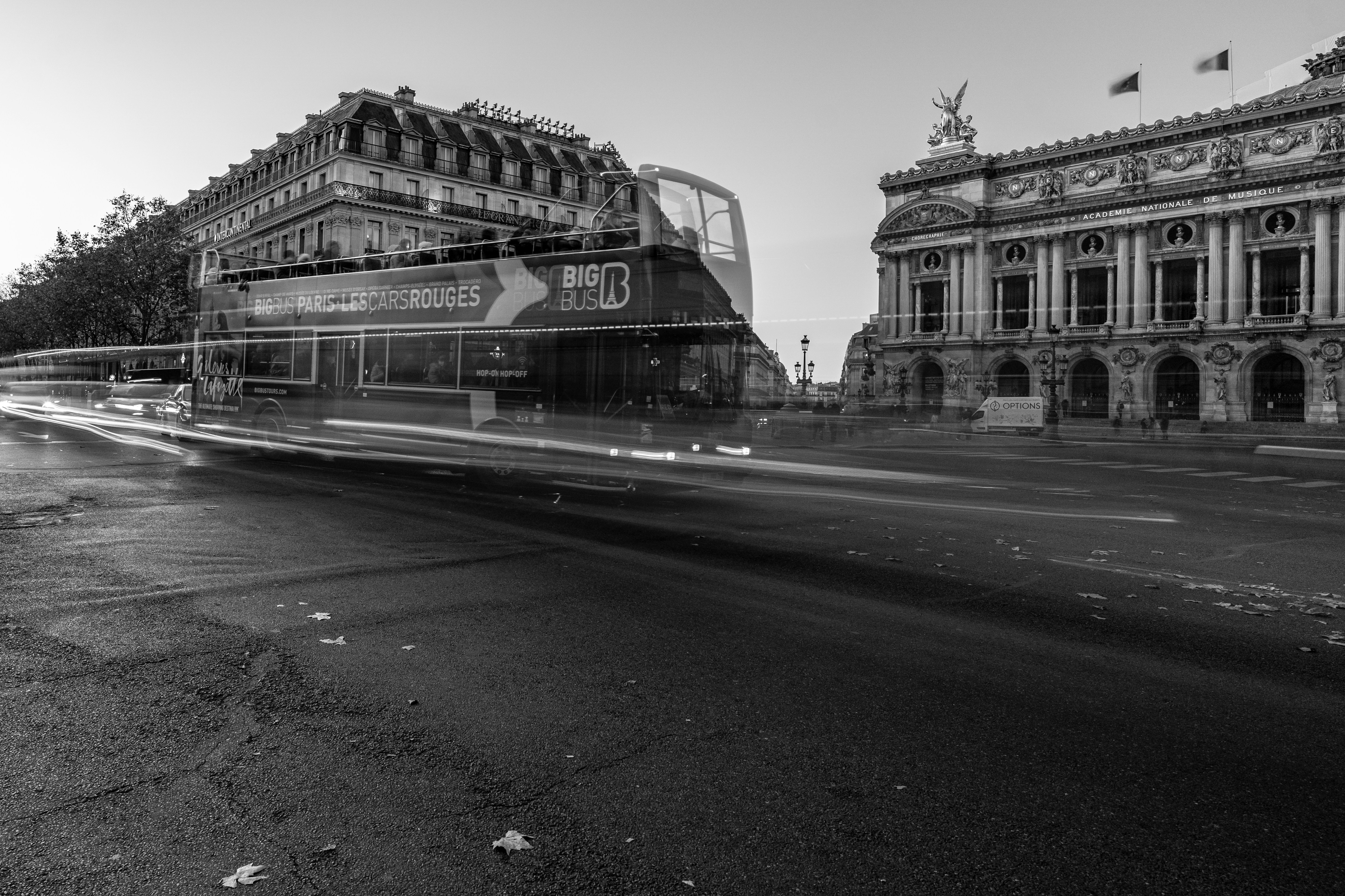 A double-decker bus in motion blurs against the backdrop of historic architecture, capturing the essence of city life. Black and white tones emphasize the contrast between movement and stillness.