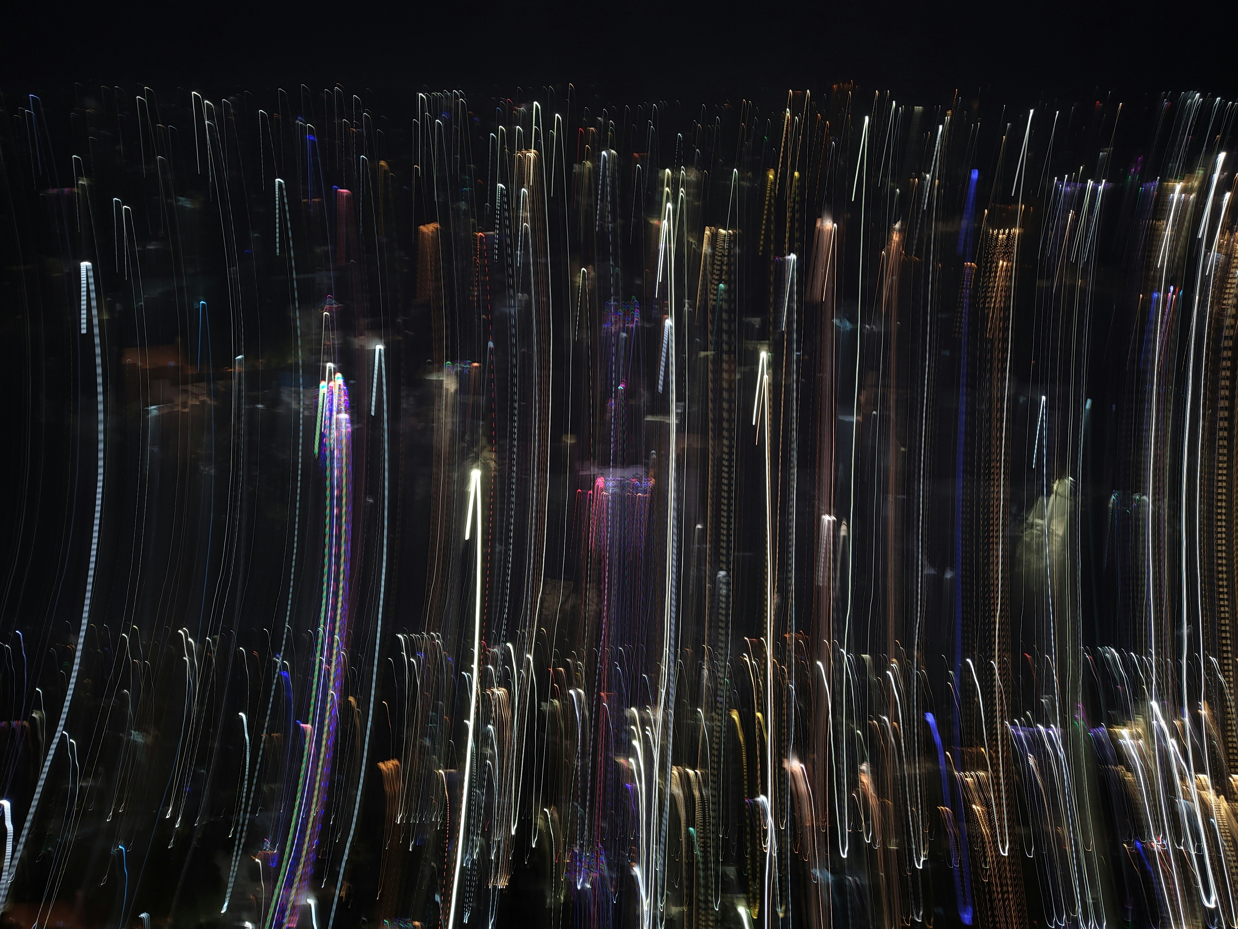 Vibrant light trails stretch vertically across a dark urban landscape.