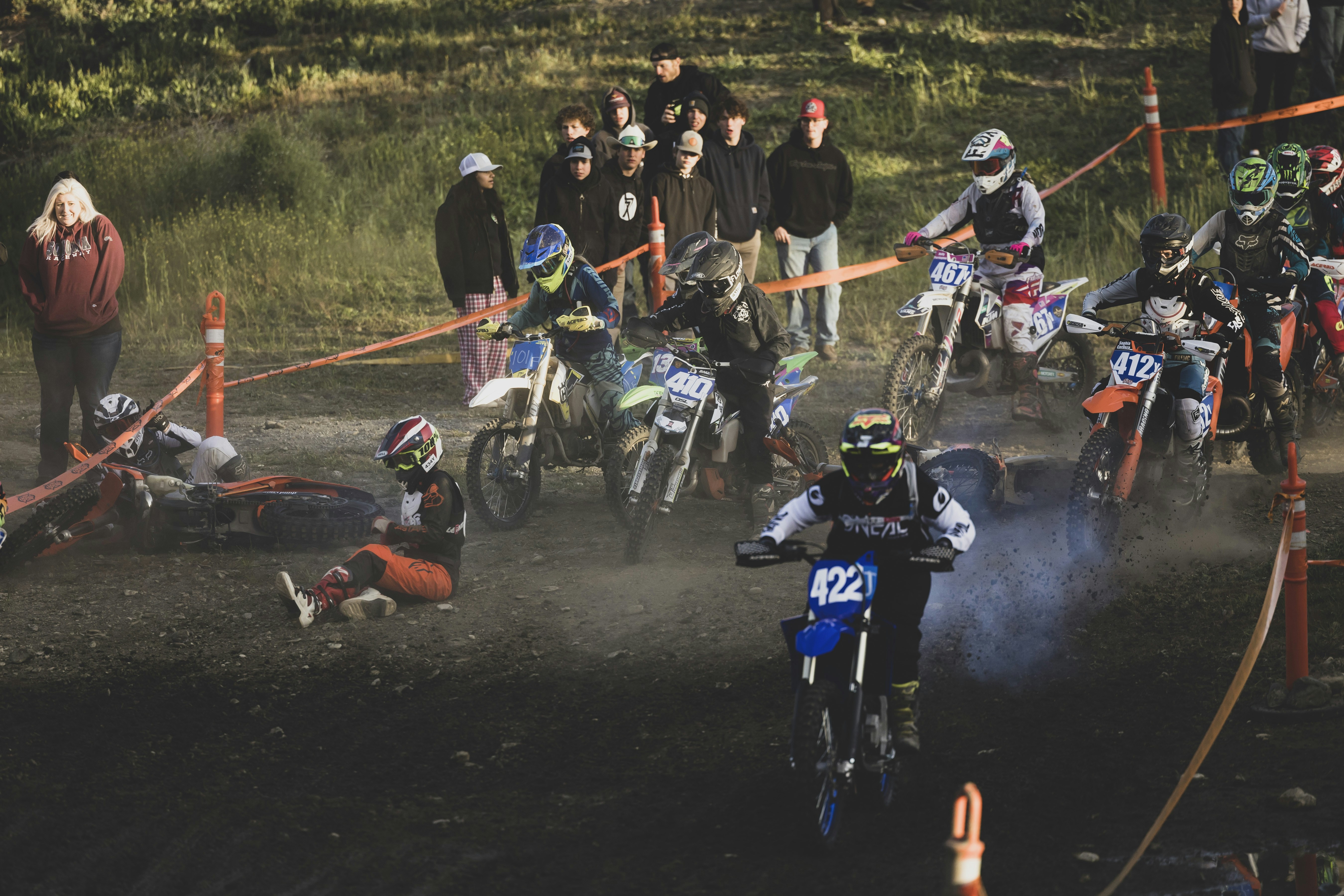 Motocross riders navigating a dirt track amidst a cloud of dust, with spectators observing the action in the background.