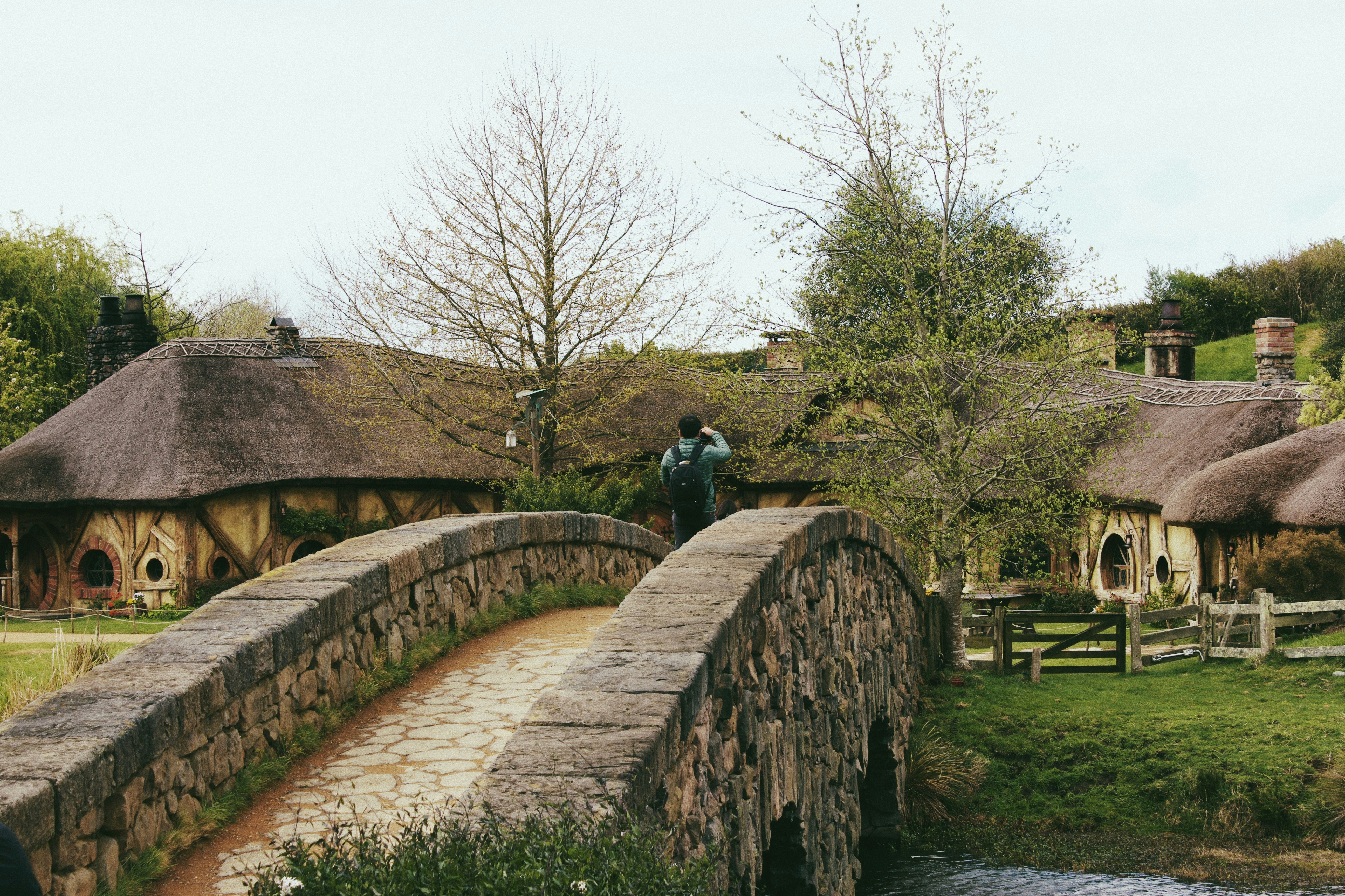 A person standing on a stone bridge photo – Free Hobbiton village Image ...