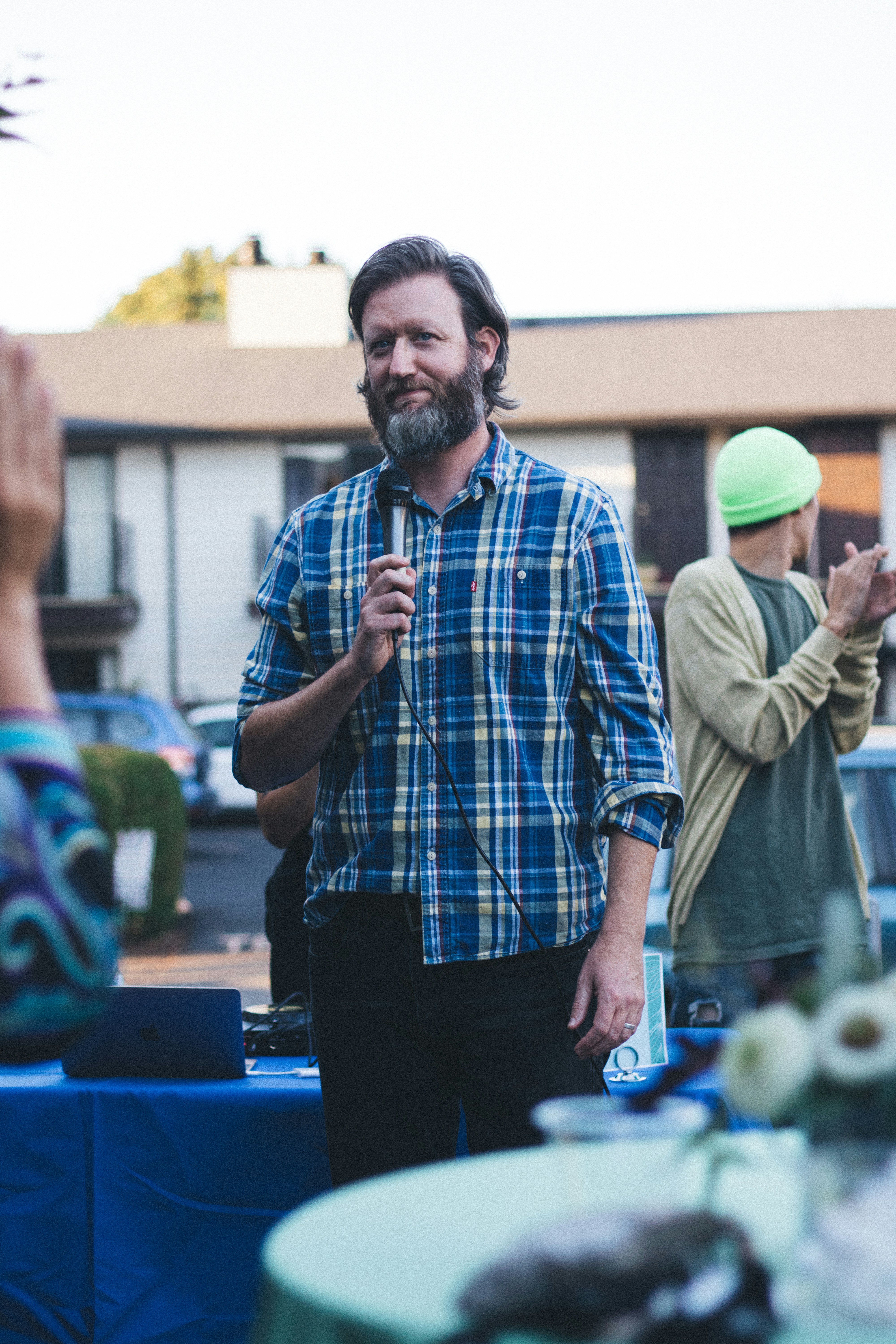 Plaid-Clad Host with Microphone Anchors an Outdoor Community Moment