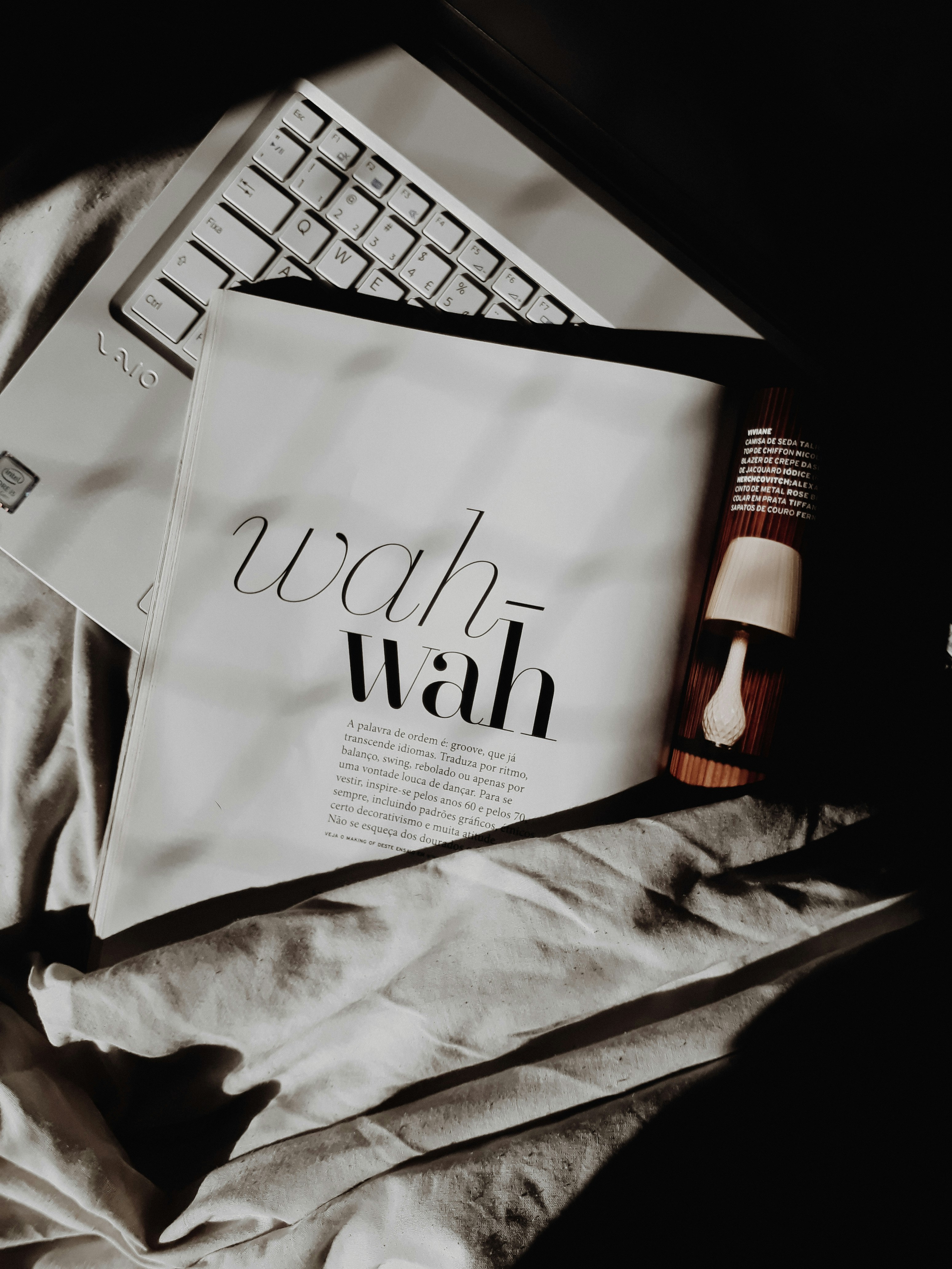 Monochrome desk still life with a laptop keyboard, a magazine bearing the 'wah-wah' typography, and a paintbrush resting on the page.