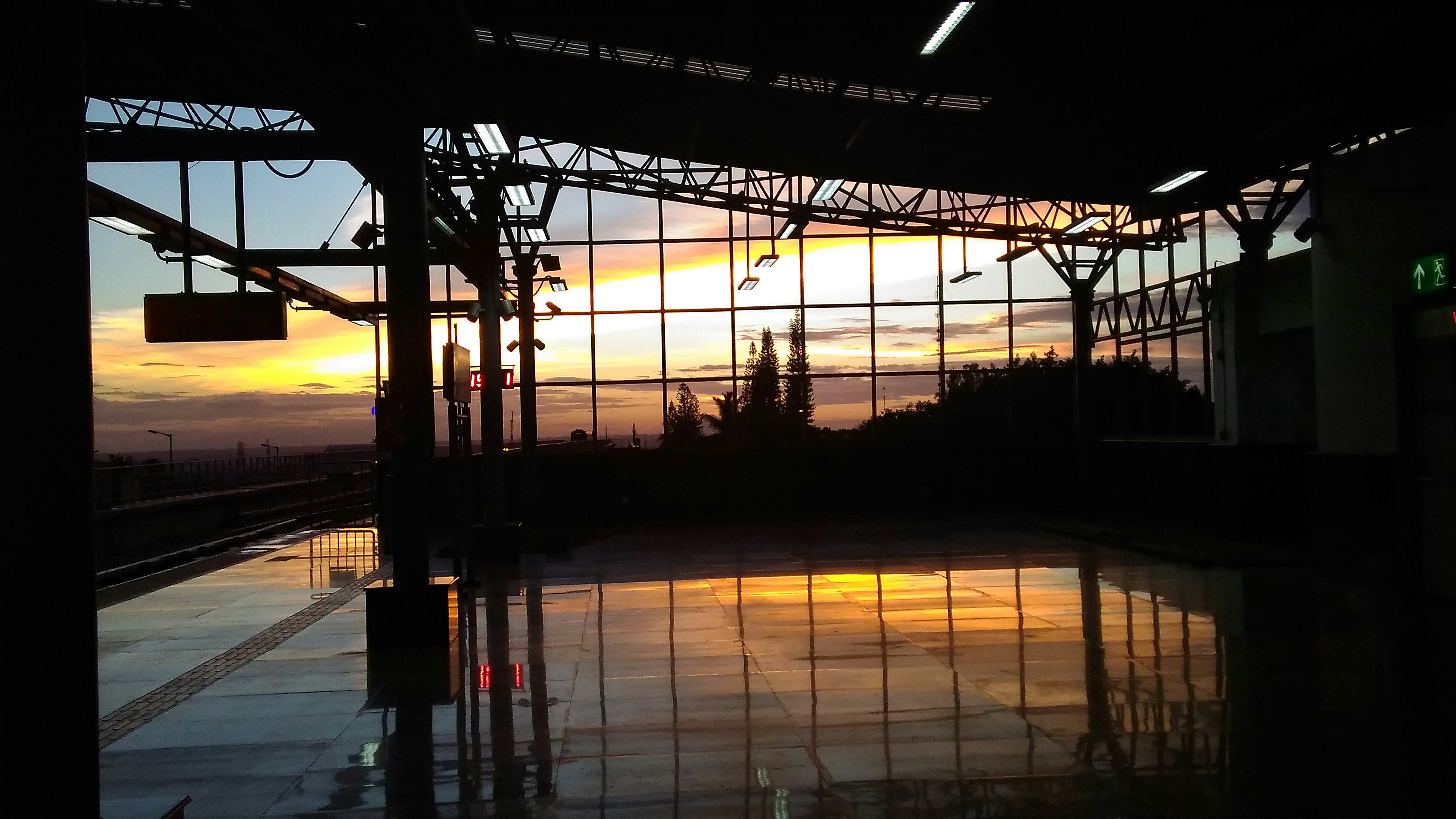 Sunset view through a glass-walled train station, with vibrant hues mirrored on the polished floor.