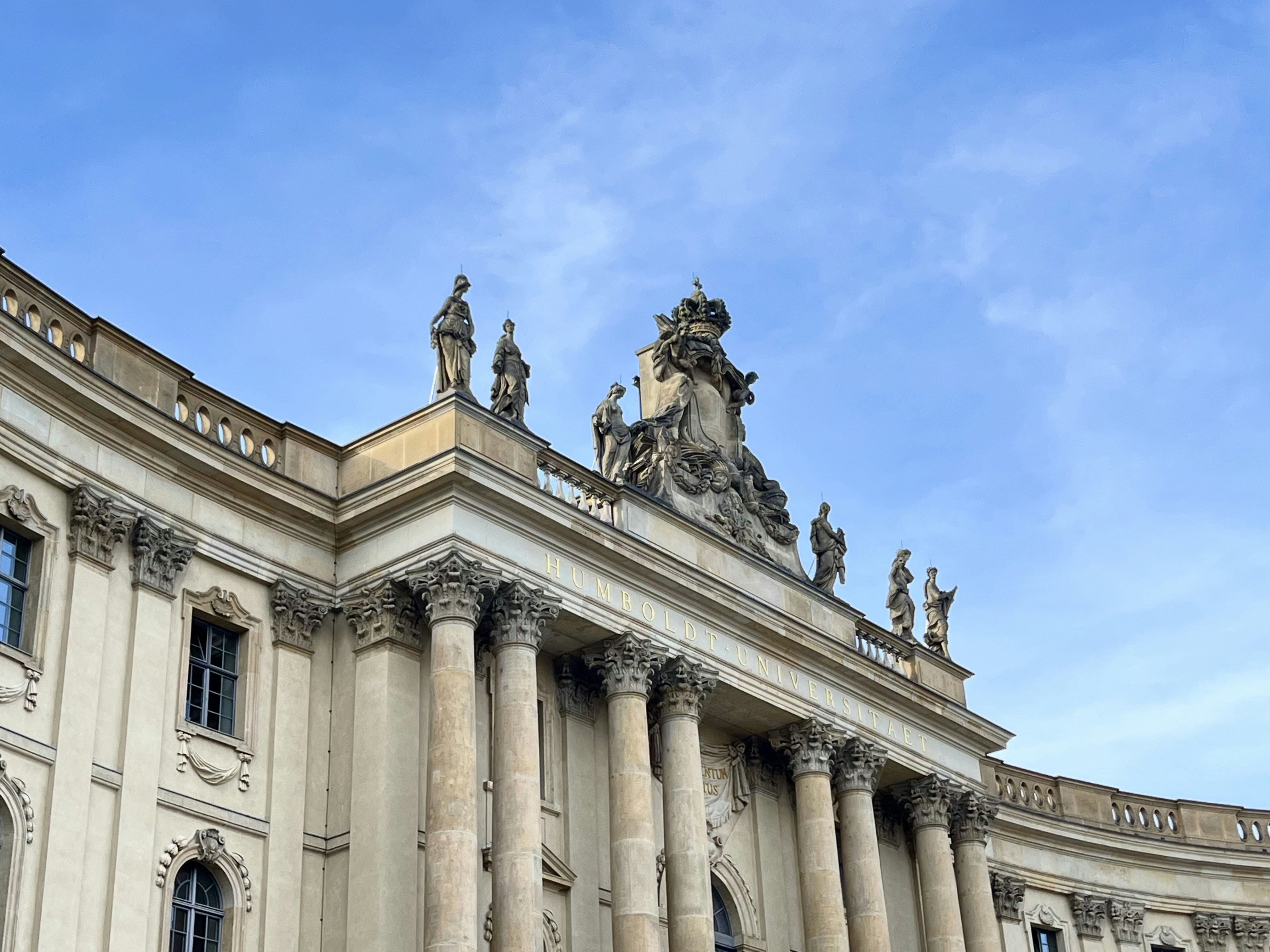 Ornate architectural facade with columns and statues under a bright blue sky.