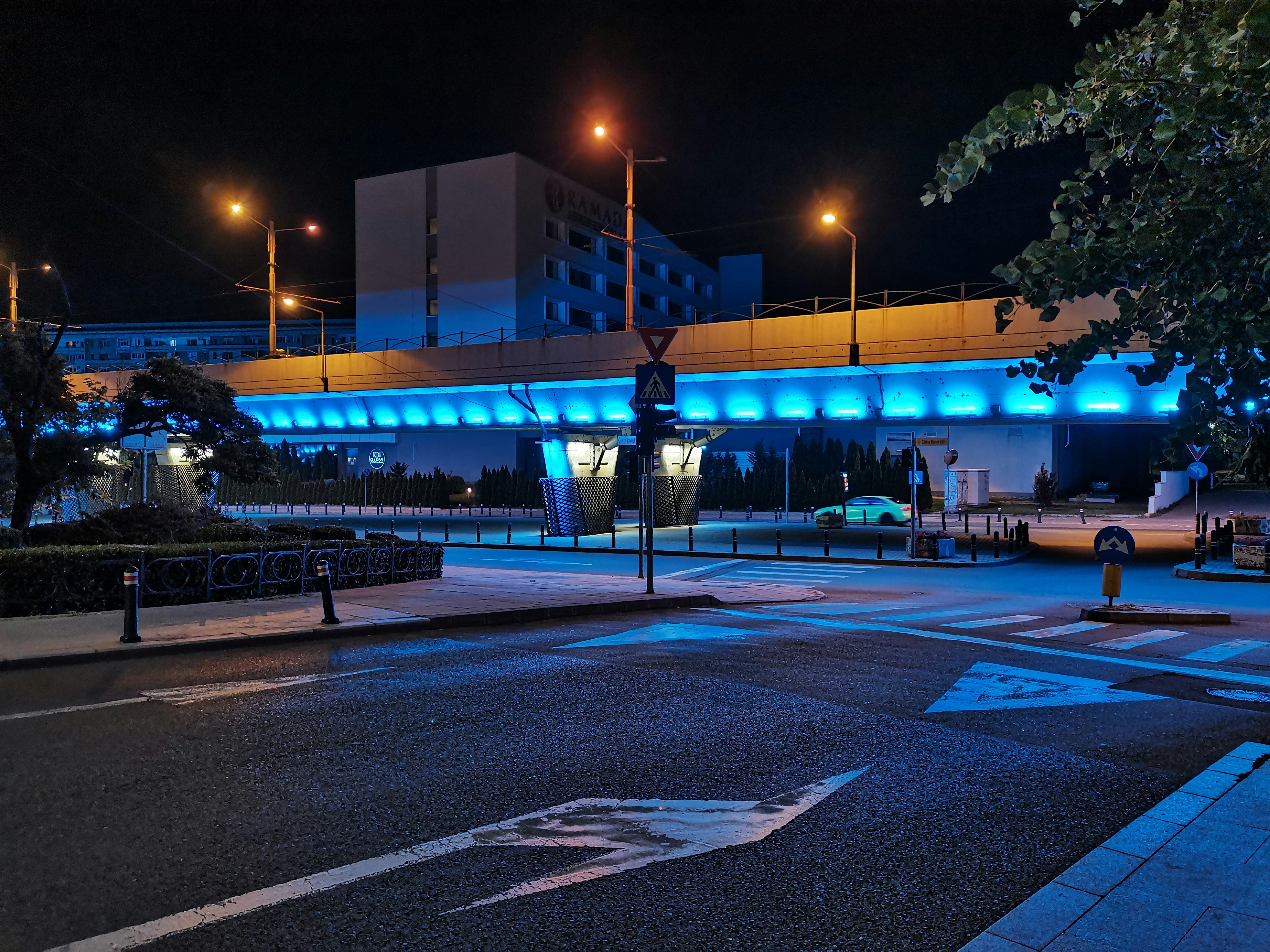 Urban street scene at night with a bridge illuminated by blue neon lights.