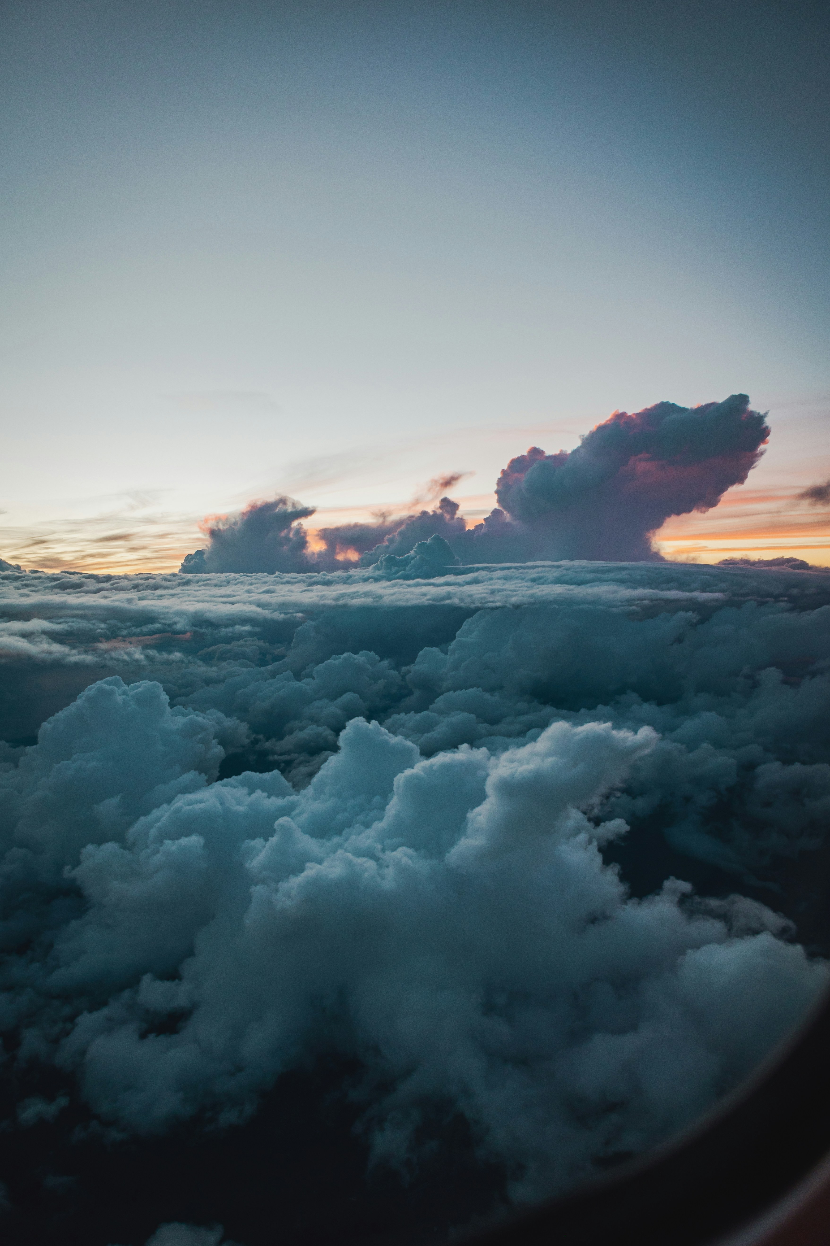 Fluffy white clouds stretch across the horizon, illuminated by the soft hues of sunset. The scene captures the serene beauty of the sky from above.