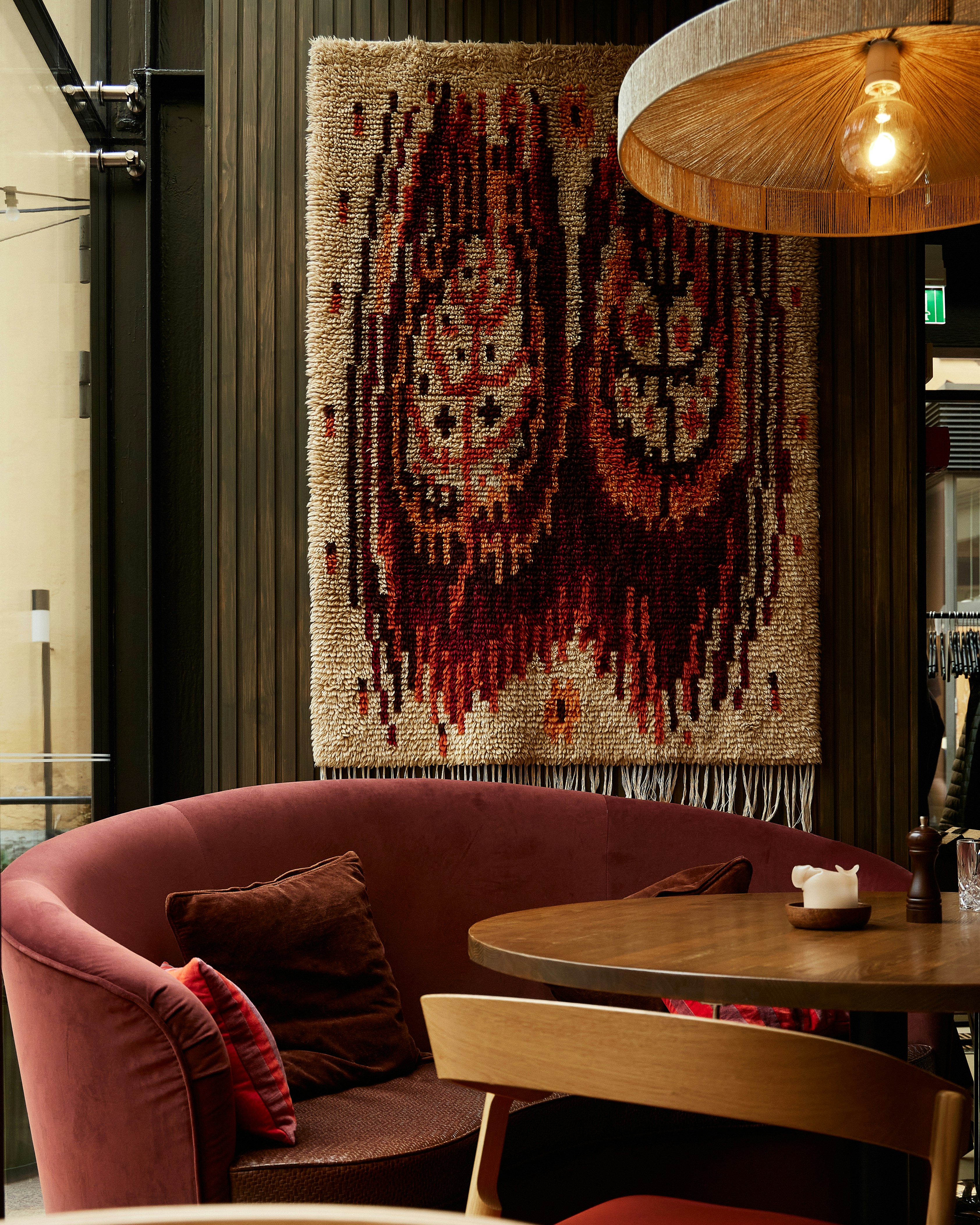 A vibrant tapestry featuring abstract designs hangs above a cozy seating area, enhancing the warm ambiance of the space.