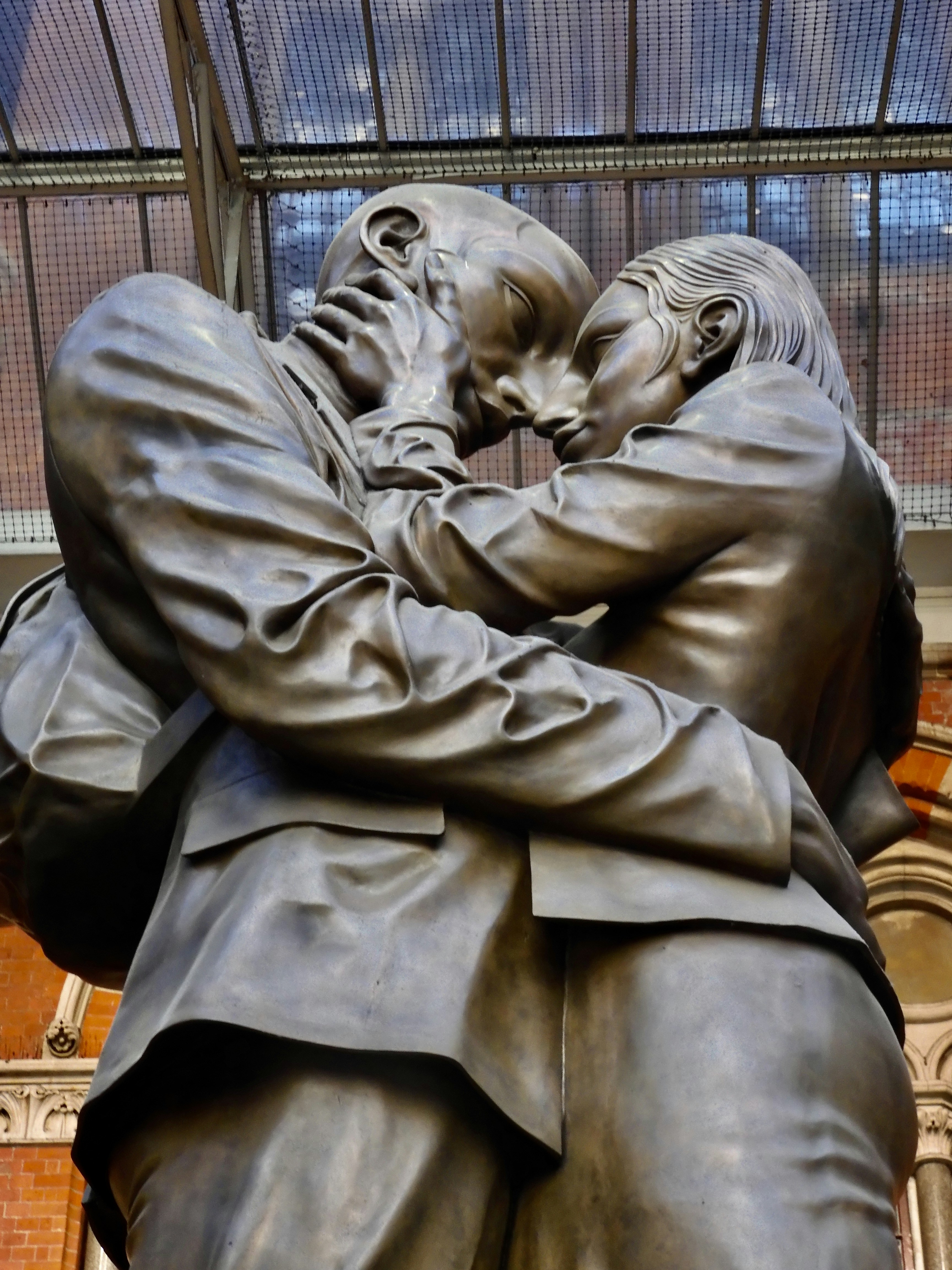 Bronze sculpture of a couple locked in a tender kiss, showcasing intricate details of their expressions and attire. The artwork captures the essence of love and intimacy.