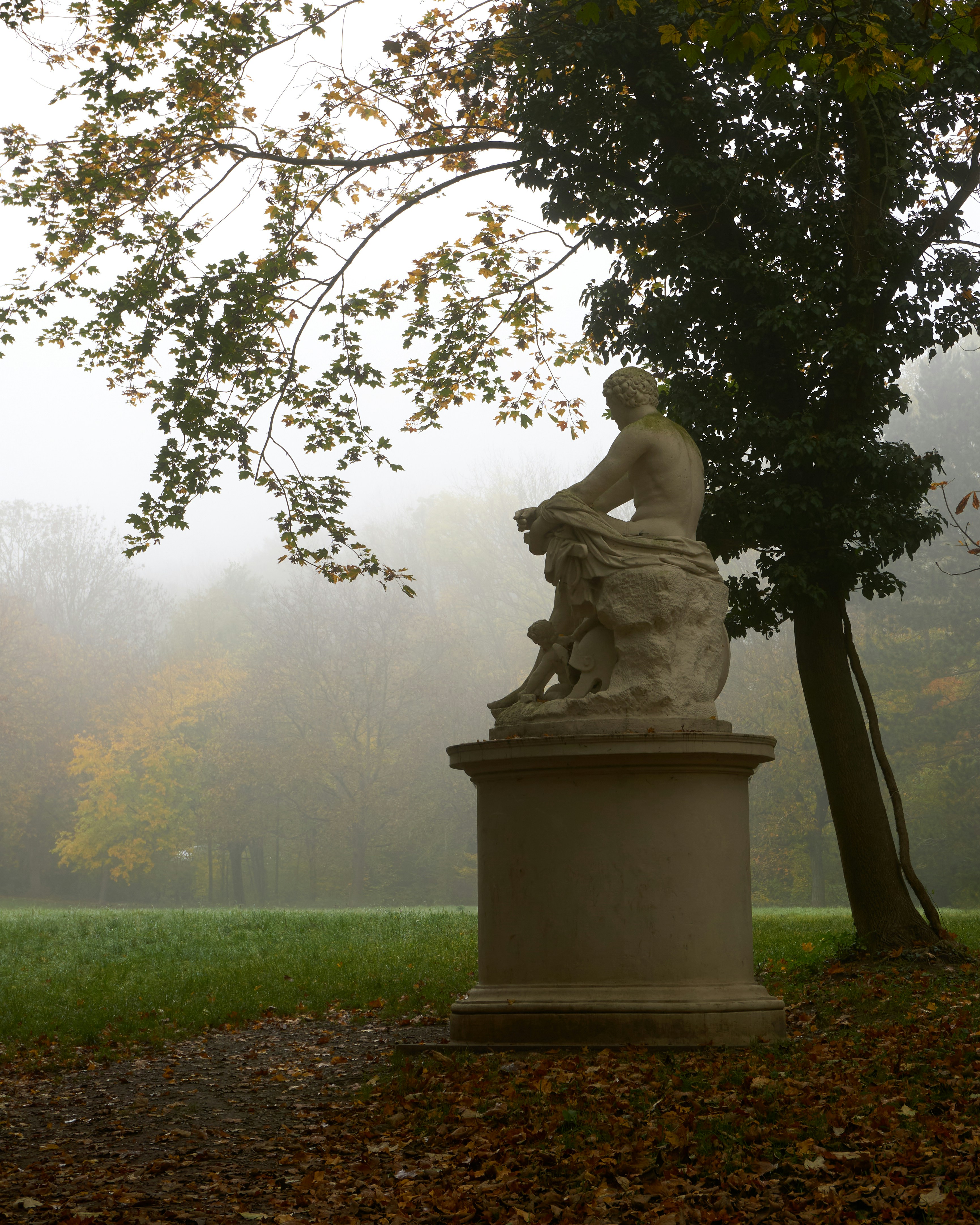 A statue of a person sitting on a stone pedestal in a park photo – Free ...
