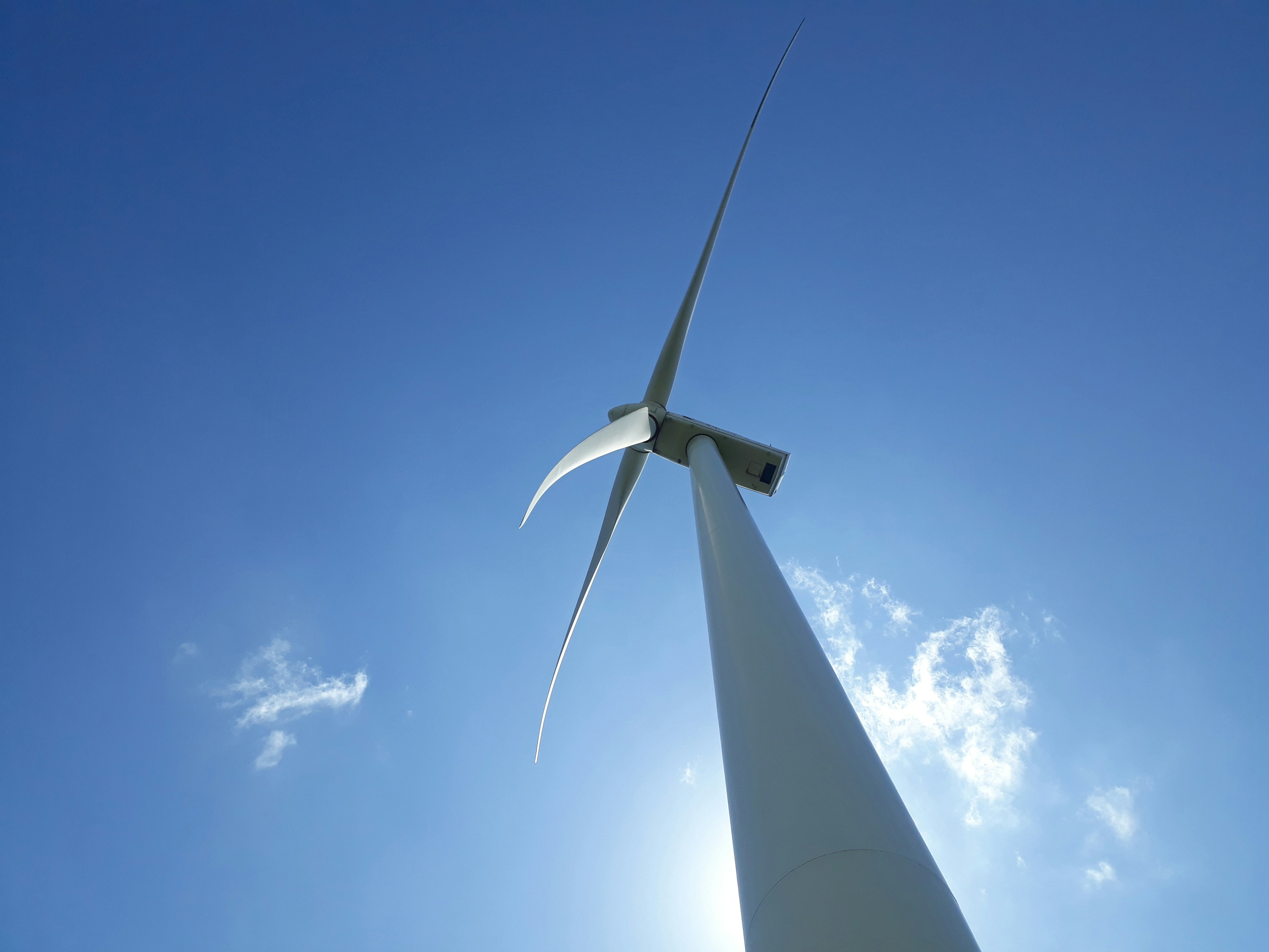 Wind turbine soaring against a clear blue sky with wispy clouds.