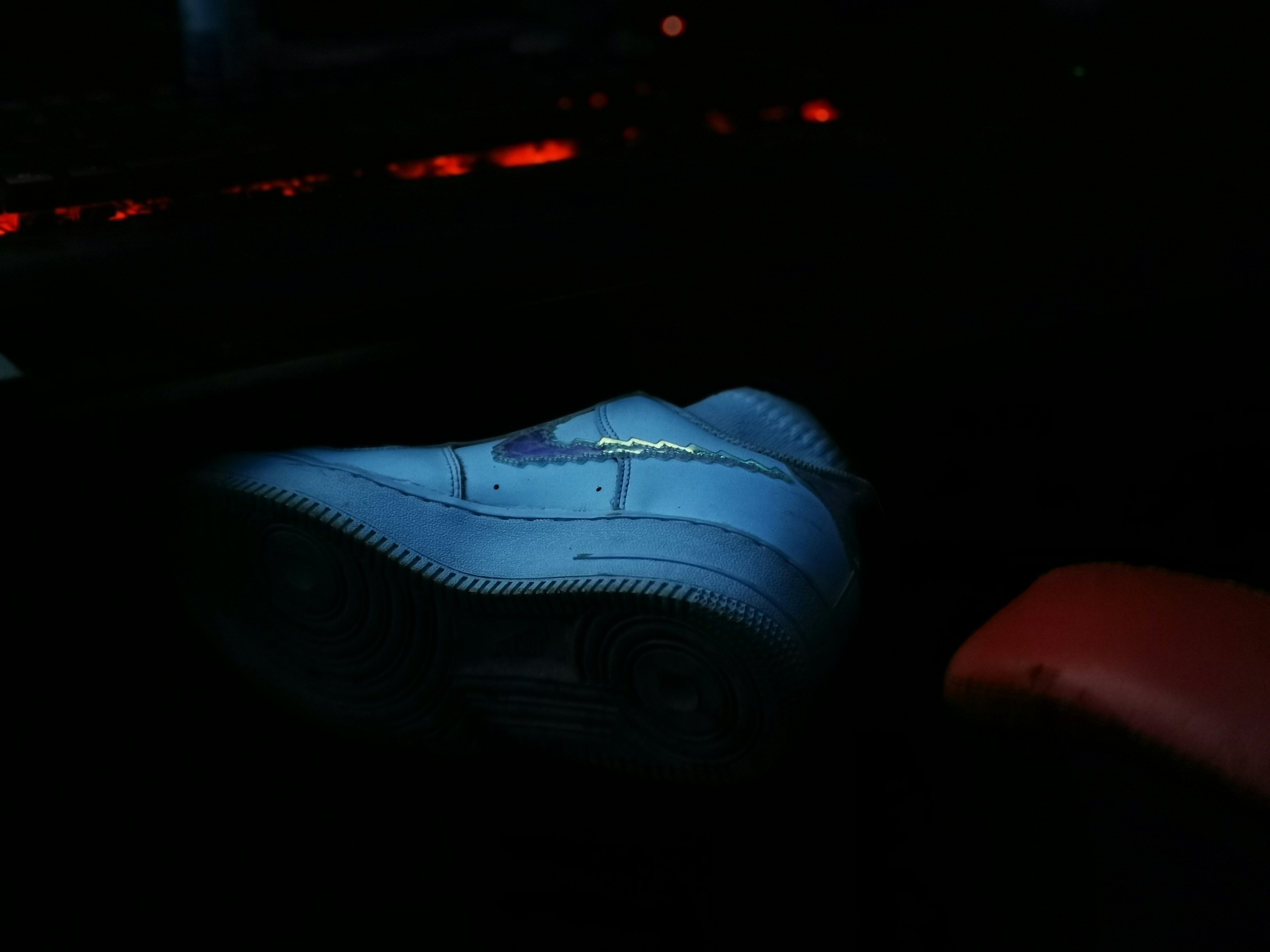 A blue sneaker illuminated in low light, contrasting with a dark background and hints of red reflections.