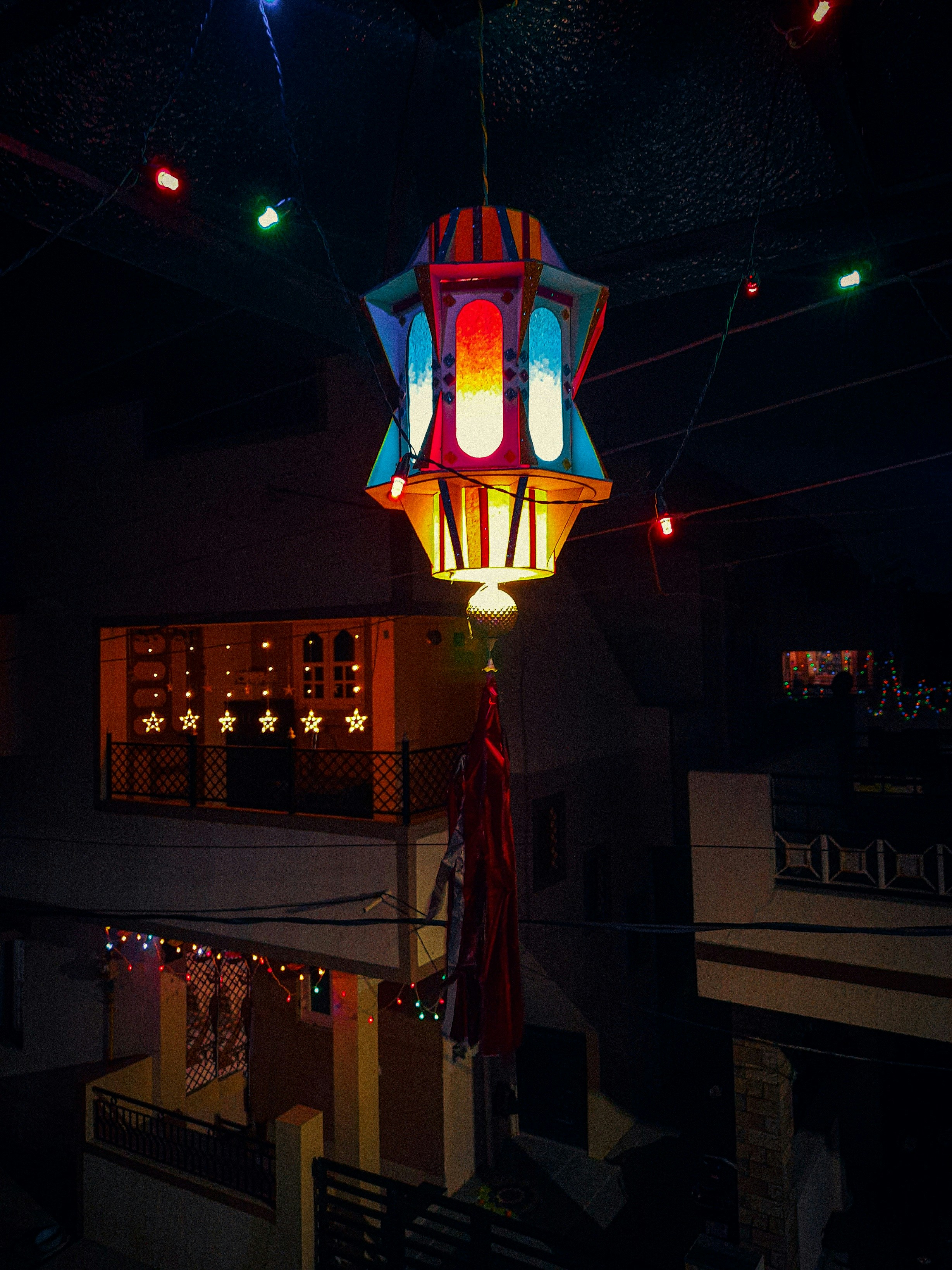 Colorful lantern hanging in a dimly lit space, surrounded by festive lights and decorations. The warm glow contrasts beautifully with the dark background.