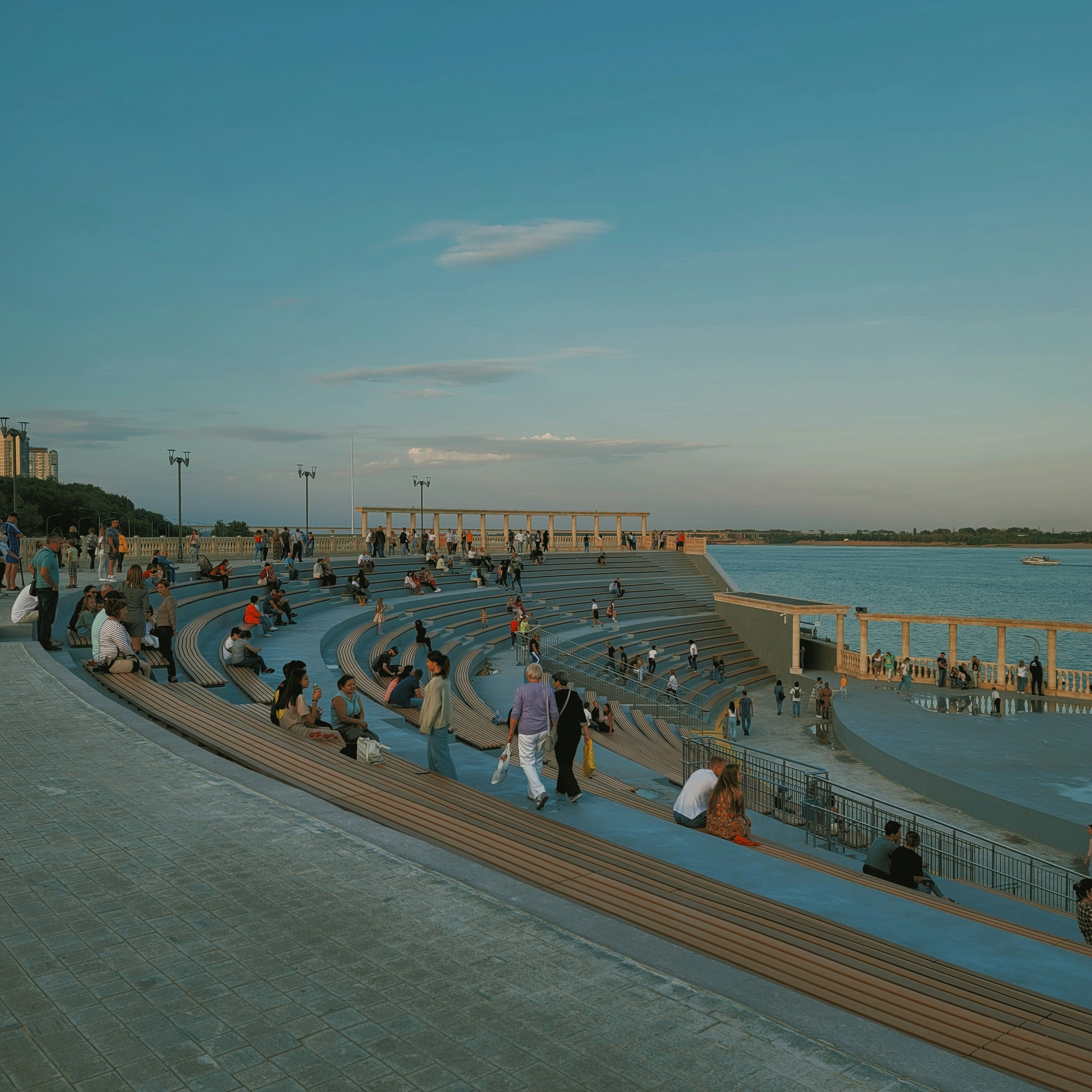 Sunlit Amphitheater by the Sea: People Gather on Tiered Steps at Dusk