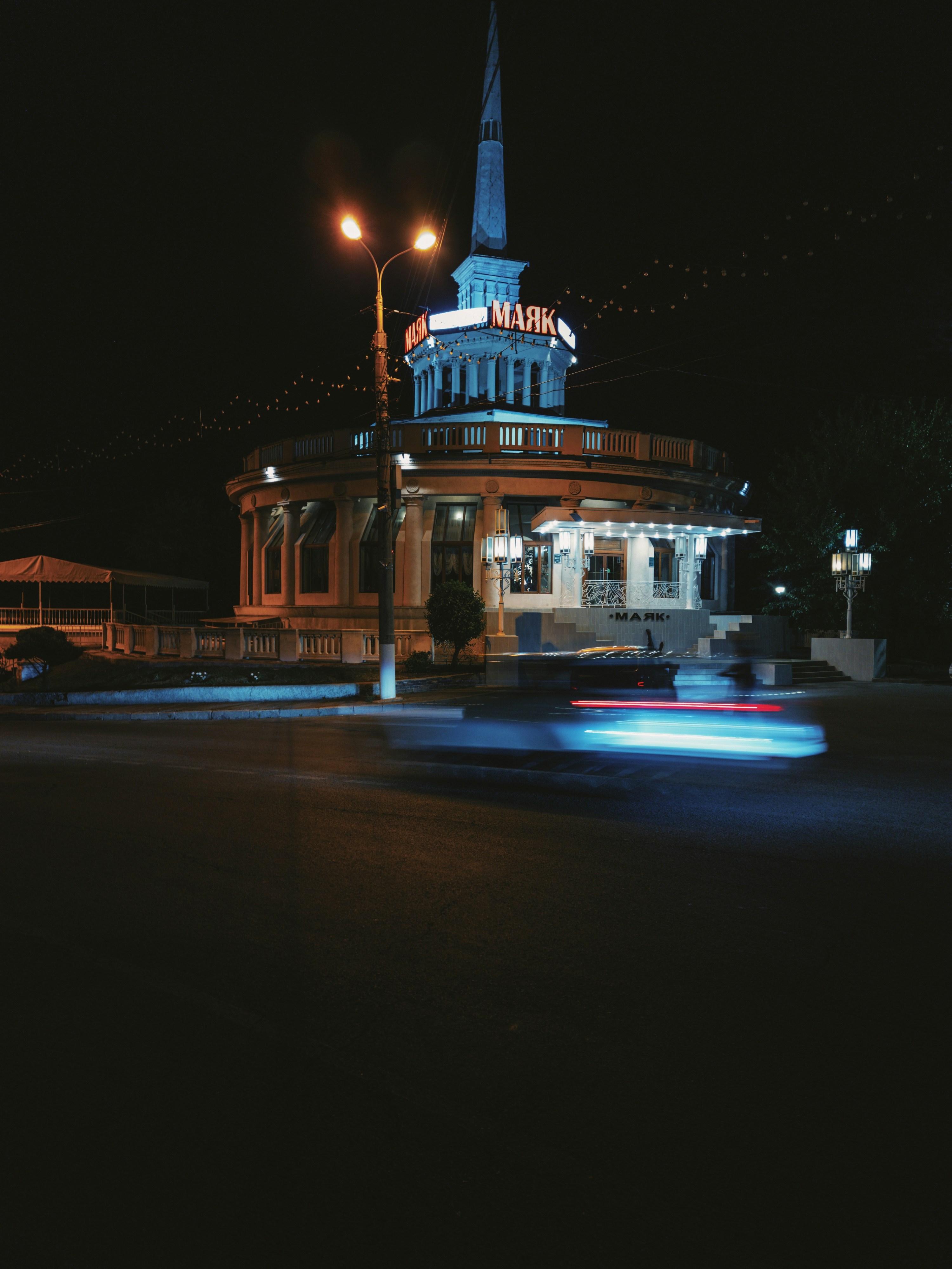 Historic building adorned with blue neon lights, capturing the essence of nightlife. A car passes by, leaving a trail of light in motion.