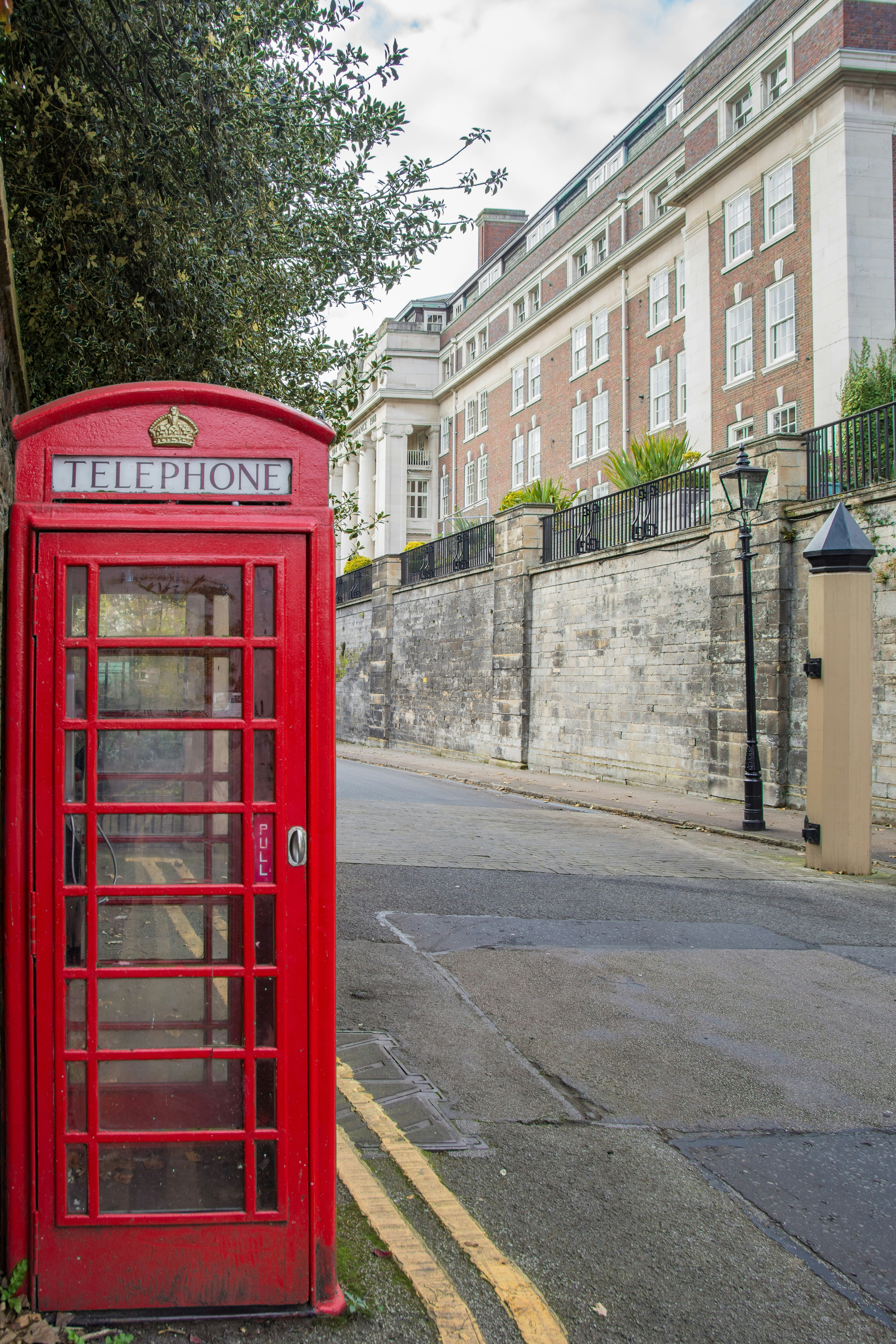 Classic red K6 telephone booth beside a historic brick building on a quiet street.