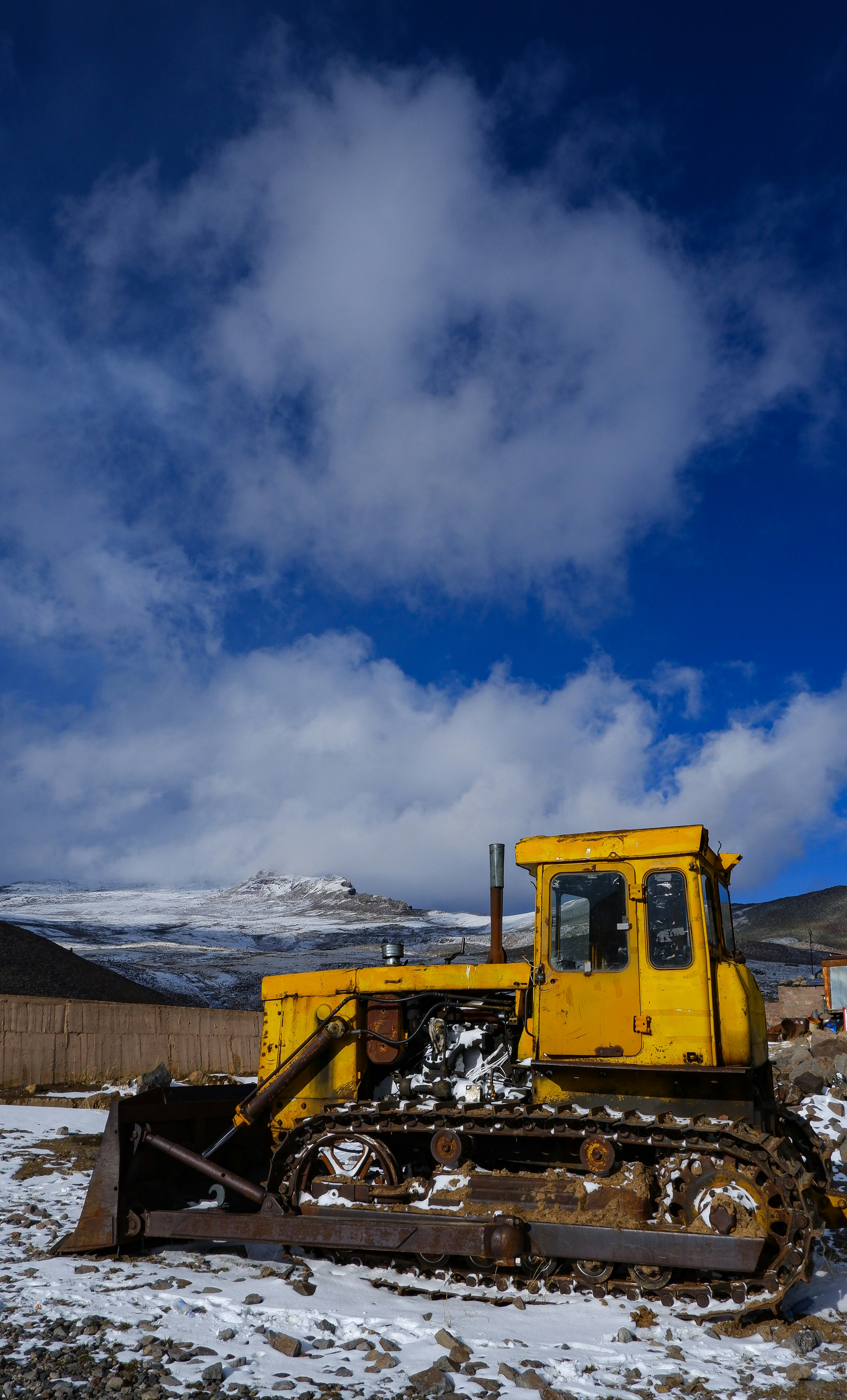 Yellow bulldozer rests in a snowy workyard under a blue sky