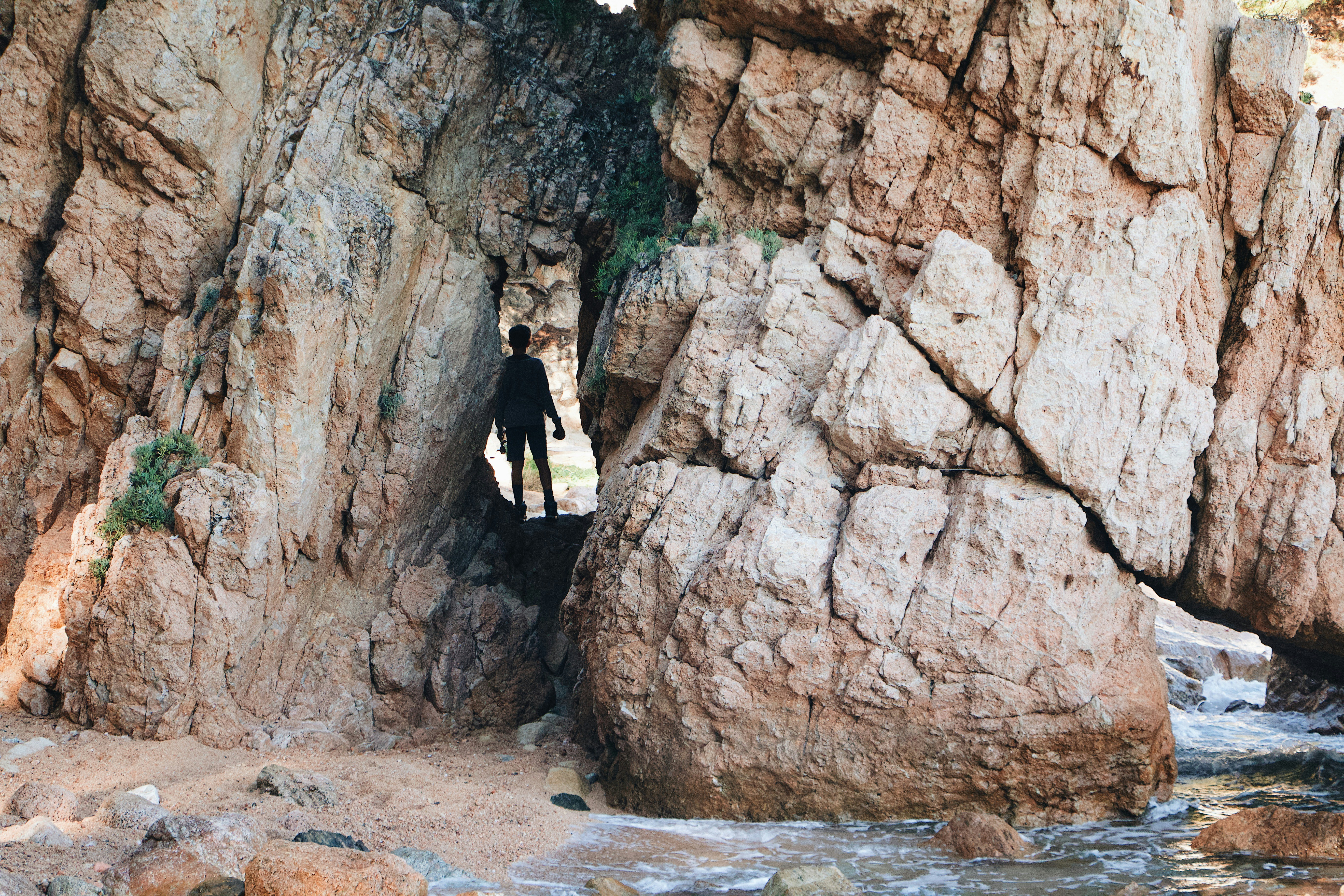 Person silhouetted in a rocky archway by the seaside.