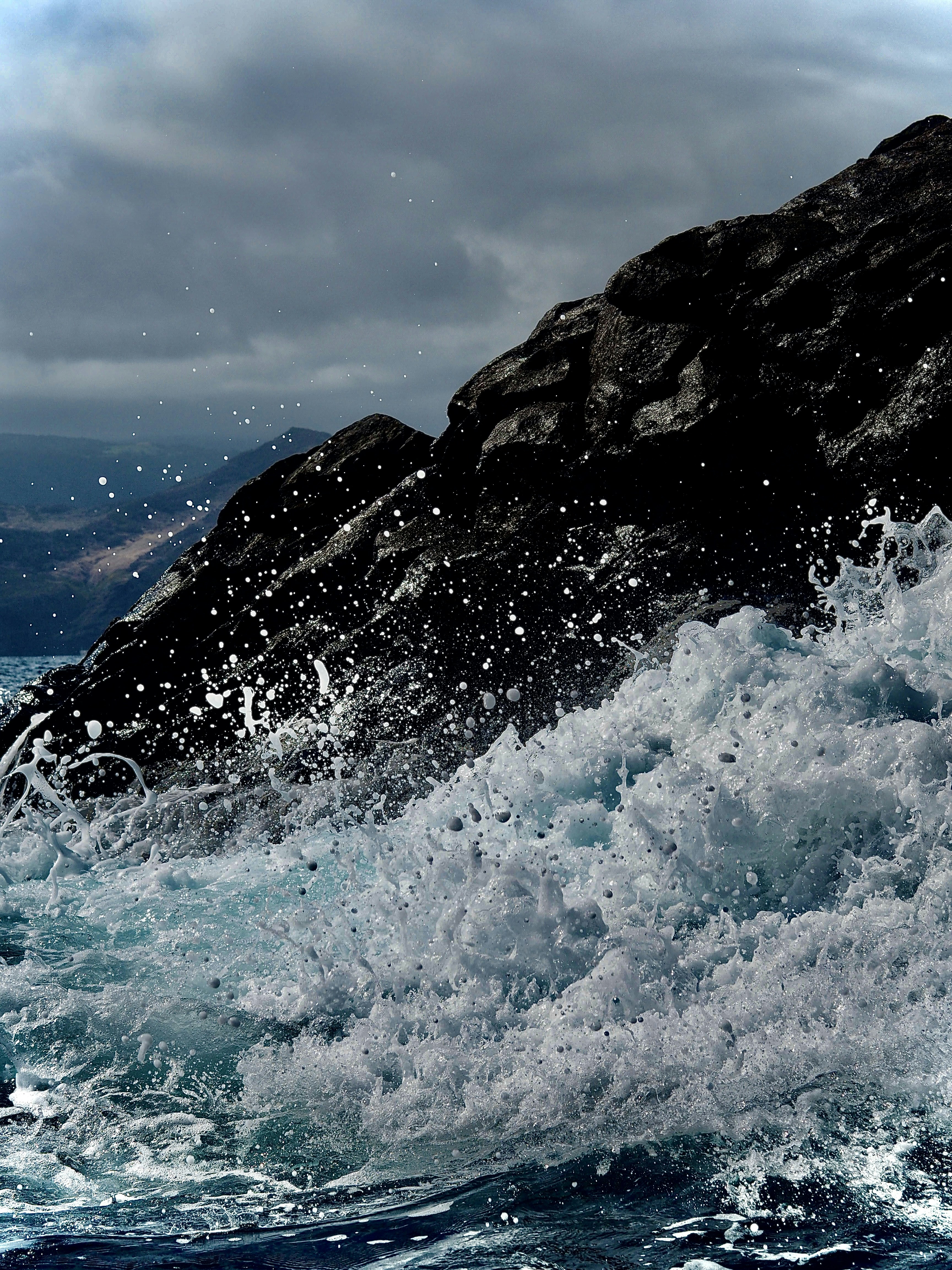 Powerful waves crash against a rugged rock formation under a moody sky. The dynamic interplay of water and stone creates a dramatic coastal scene.