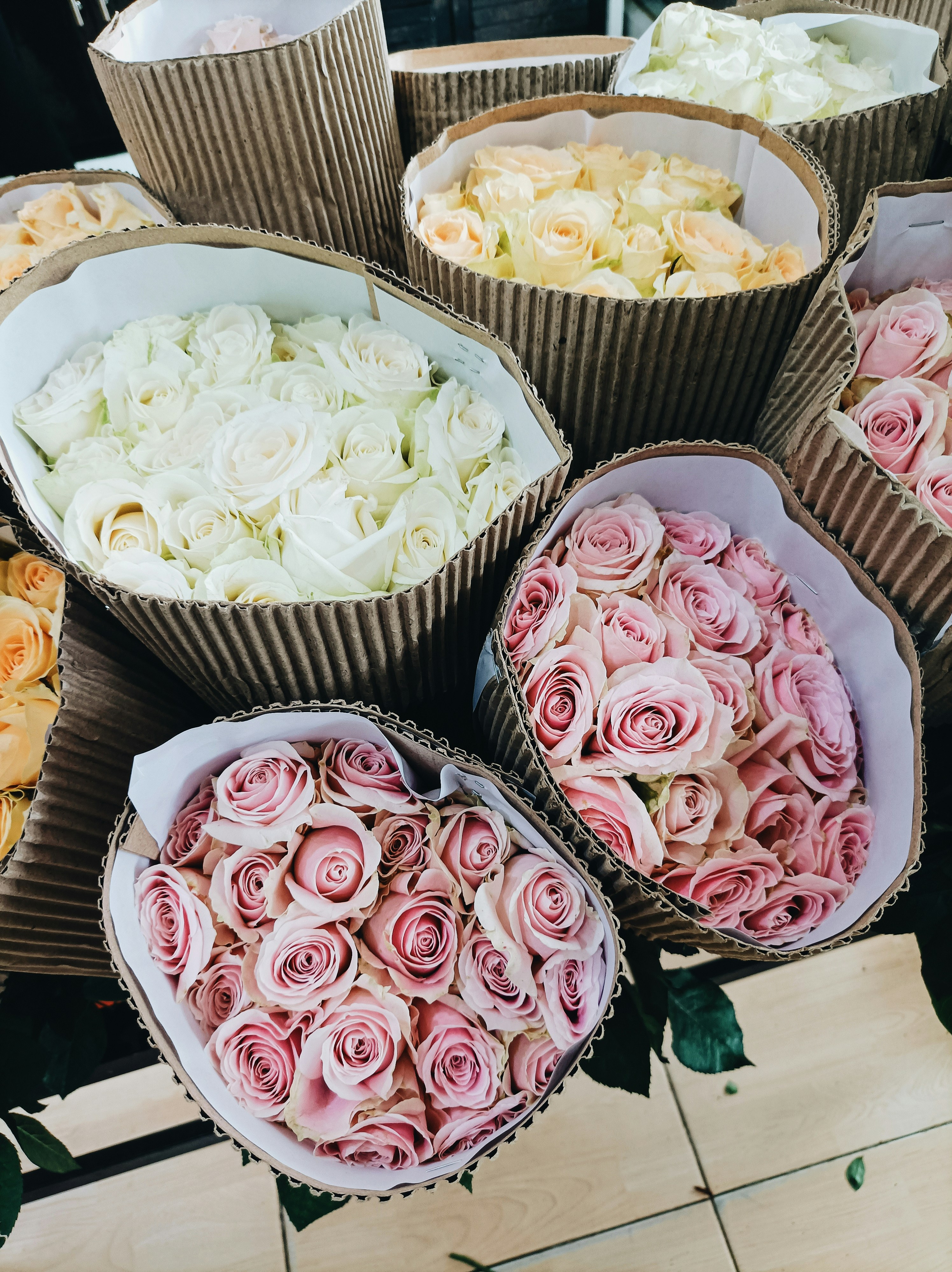 Assorted bouquets of roses in varying shades of white and pink, elegantly arranged in striped paper wrapping.