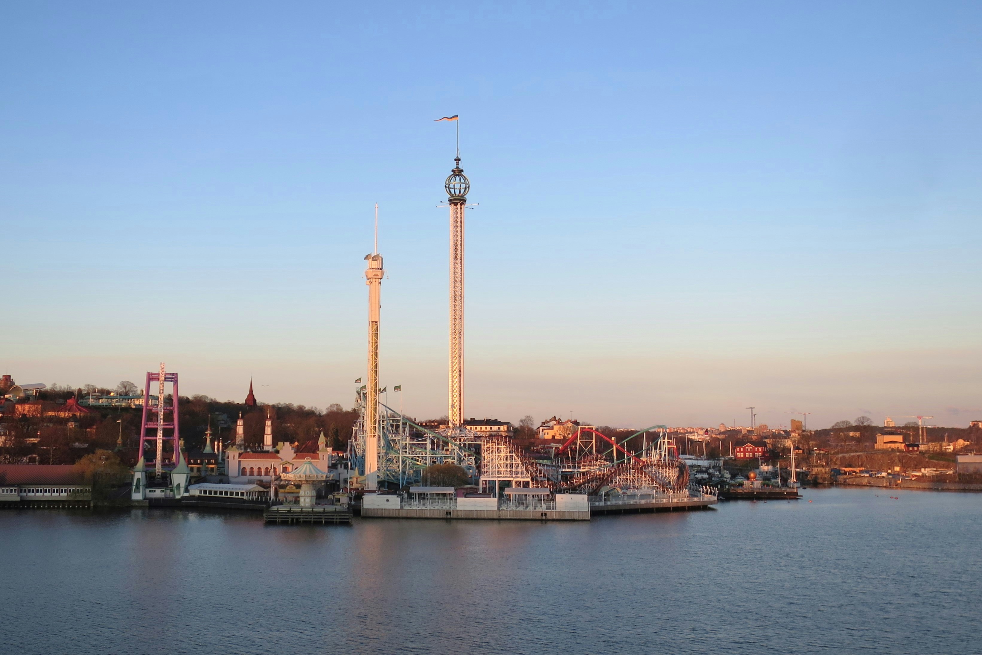 Amusement park skyline at dusk, featuring towering rides and vibrant colors reflected in the calm water below.