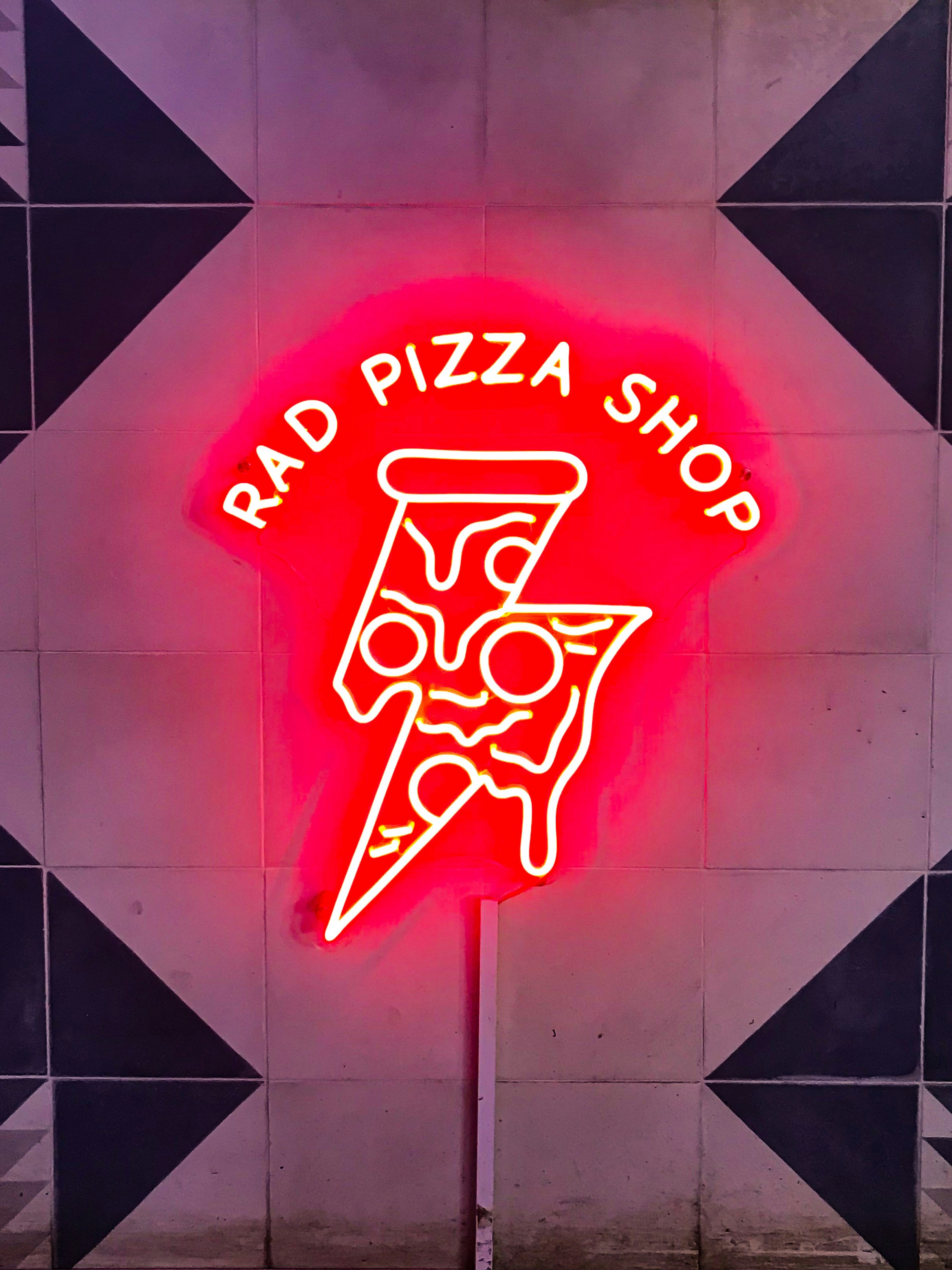Rad Pizza Shop Neon Sign Blazes Against a Geometric Tile Backdrop