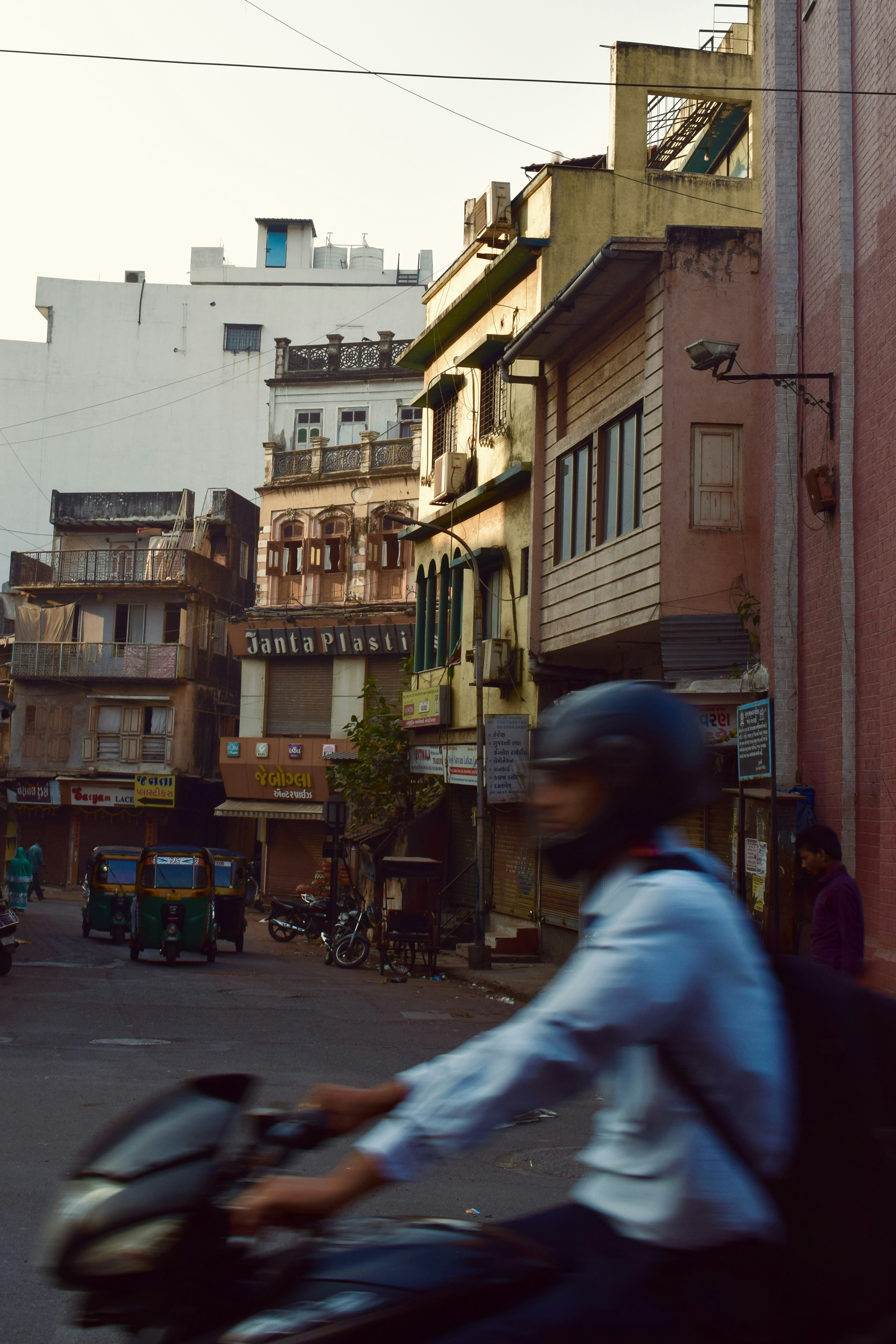 Motorcyclist rides through a narrow street lined with aged buildings and shops under morning light.