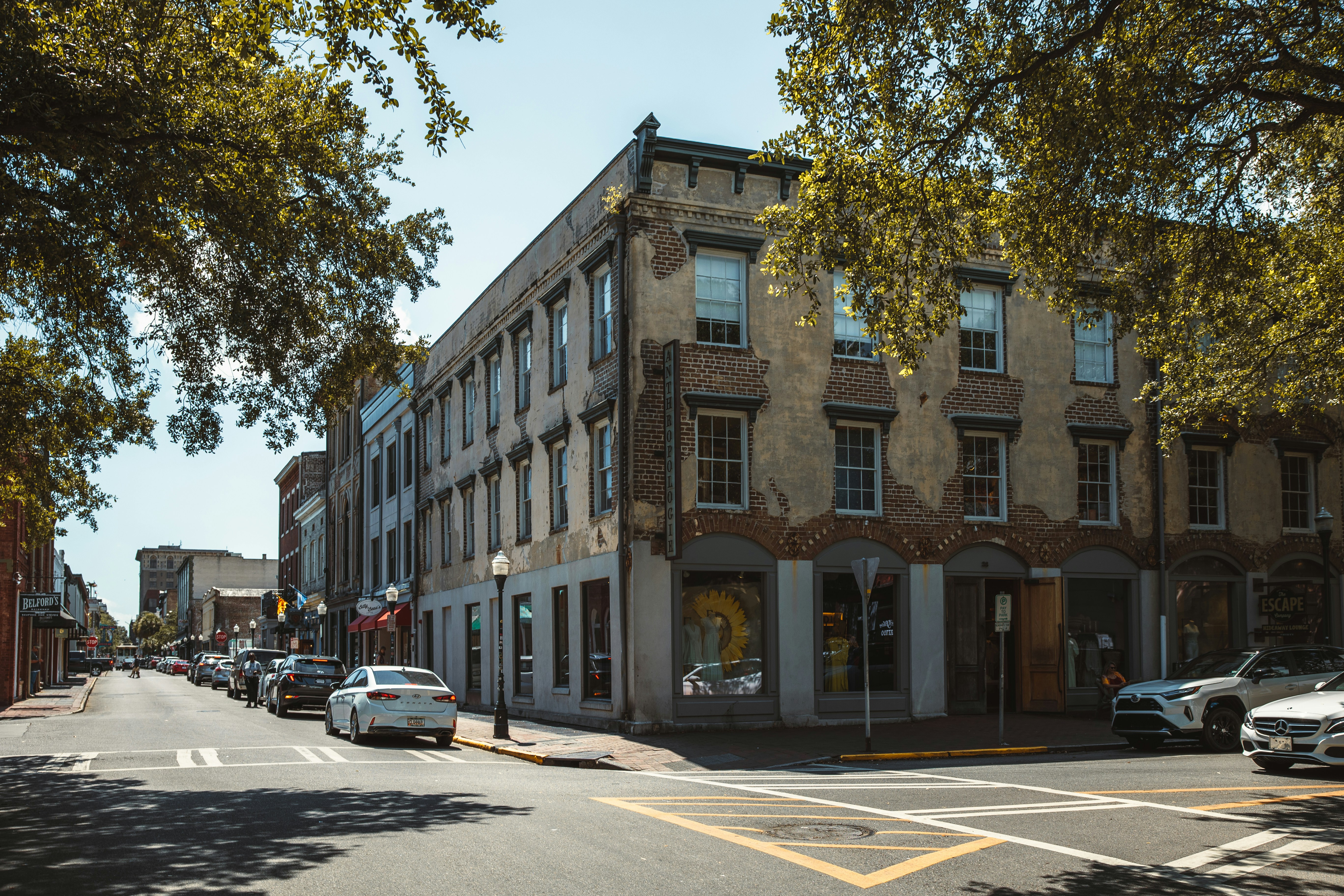 Charming historic building at a bustling street corner, framed by leafy trees and urban life. The architecture reflects a blend of history and modernity.