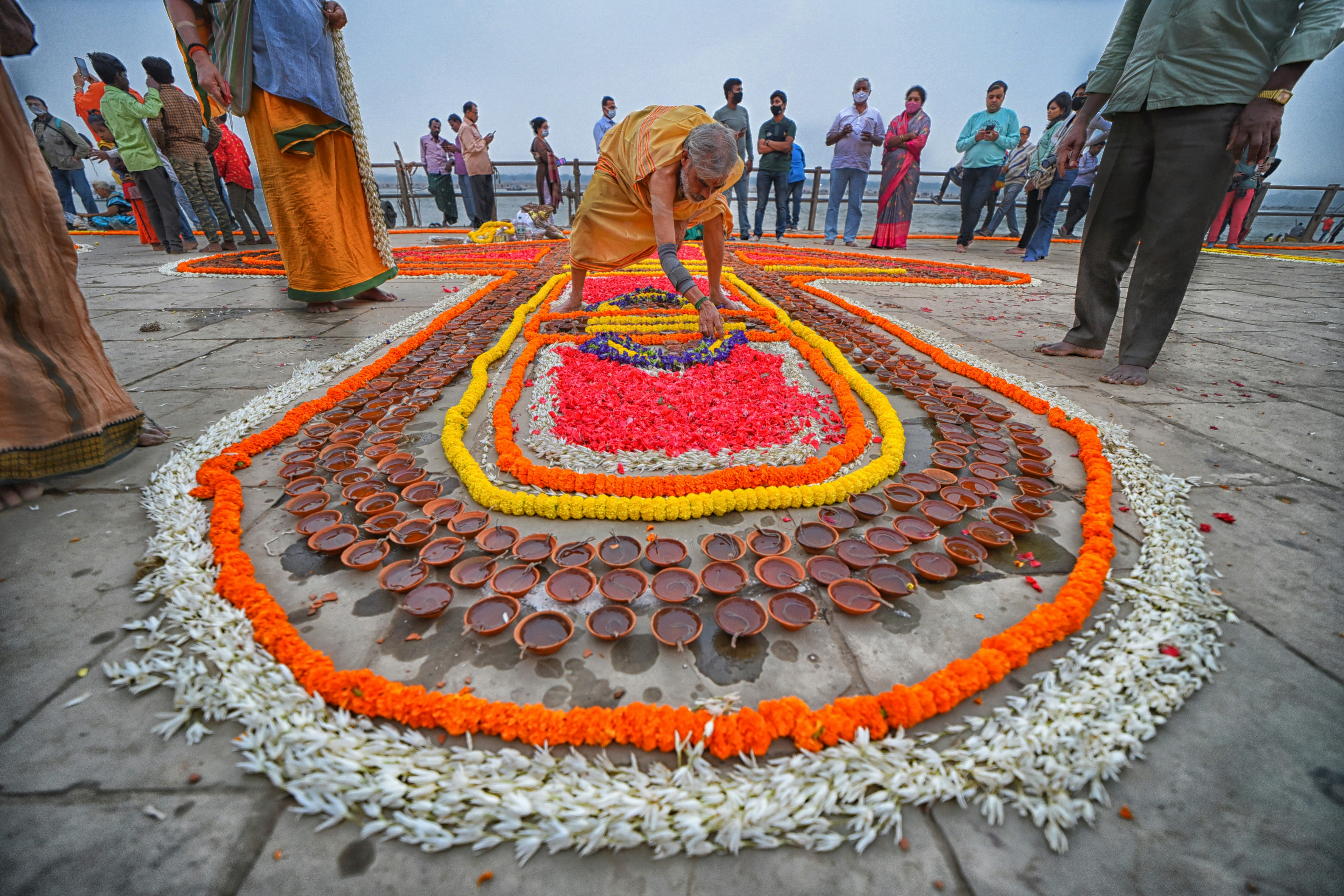 Devotee arranging lamps and flowers in an intricate pattern for a religious ceremony on the Ganges riverbank.