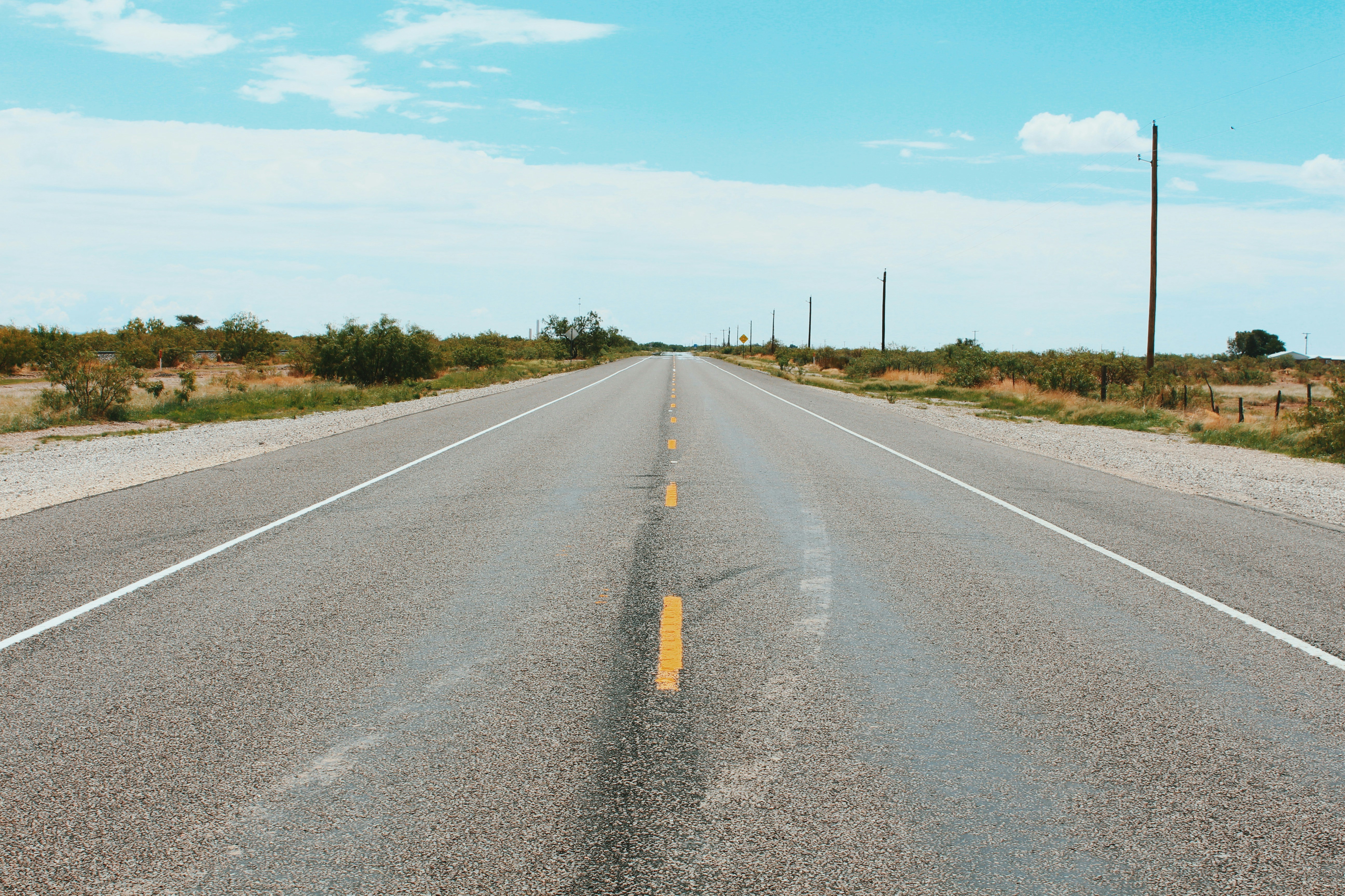 A straight highway stretches into the distance, flanked by sparse vegetation under a bright blue sky. The scene evokes a sense of freedom and adventure.