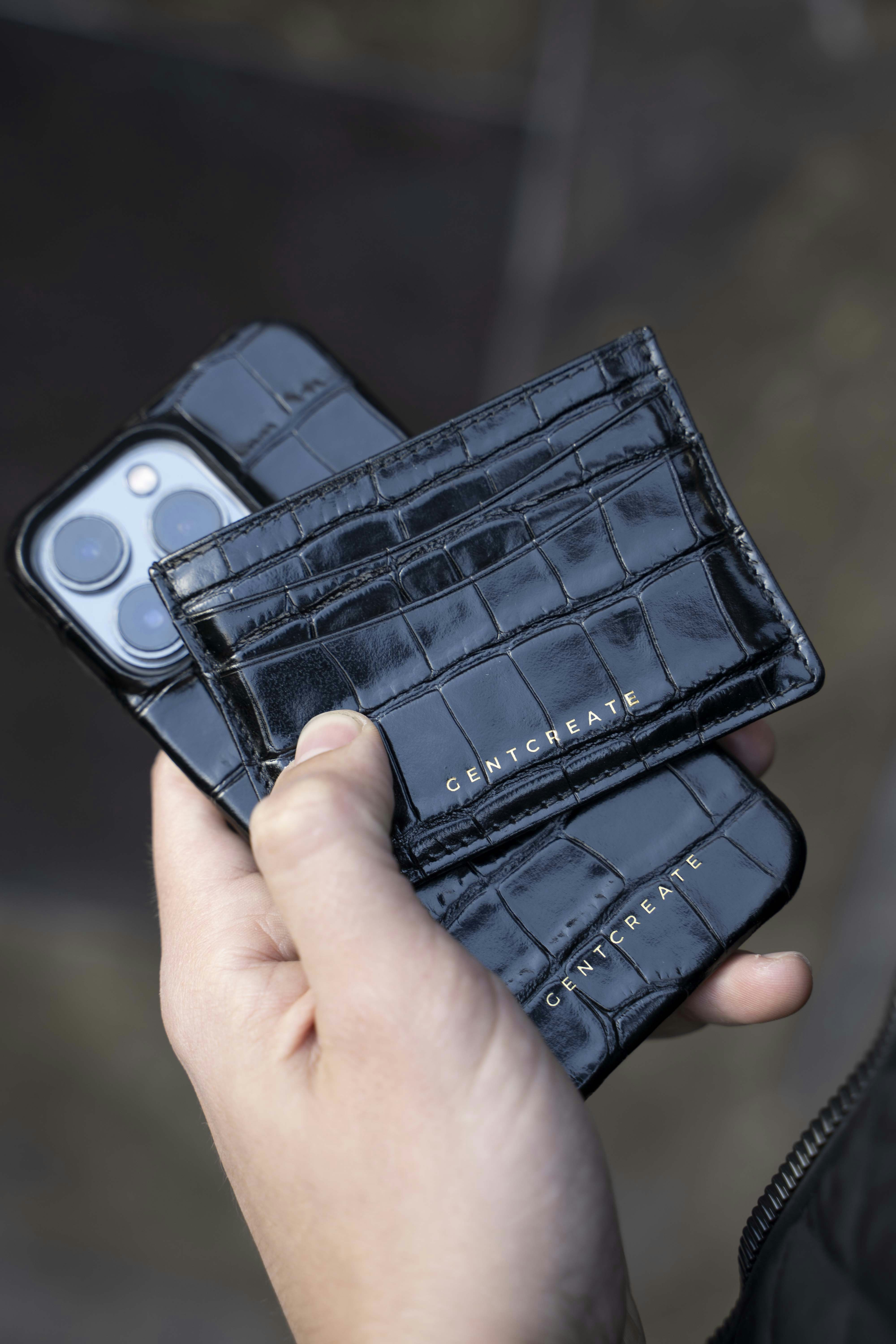 Man holding black leather accessories in the left hand, iPhone 14 phone case, and business card holder.