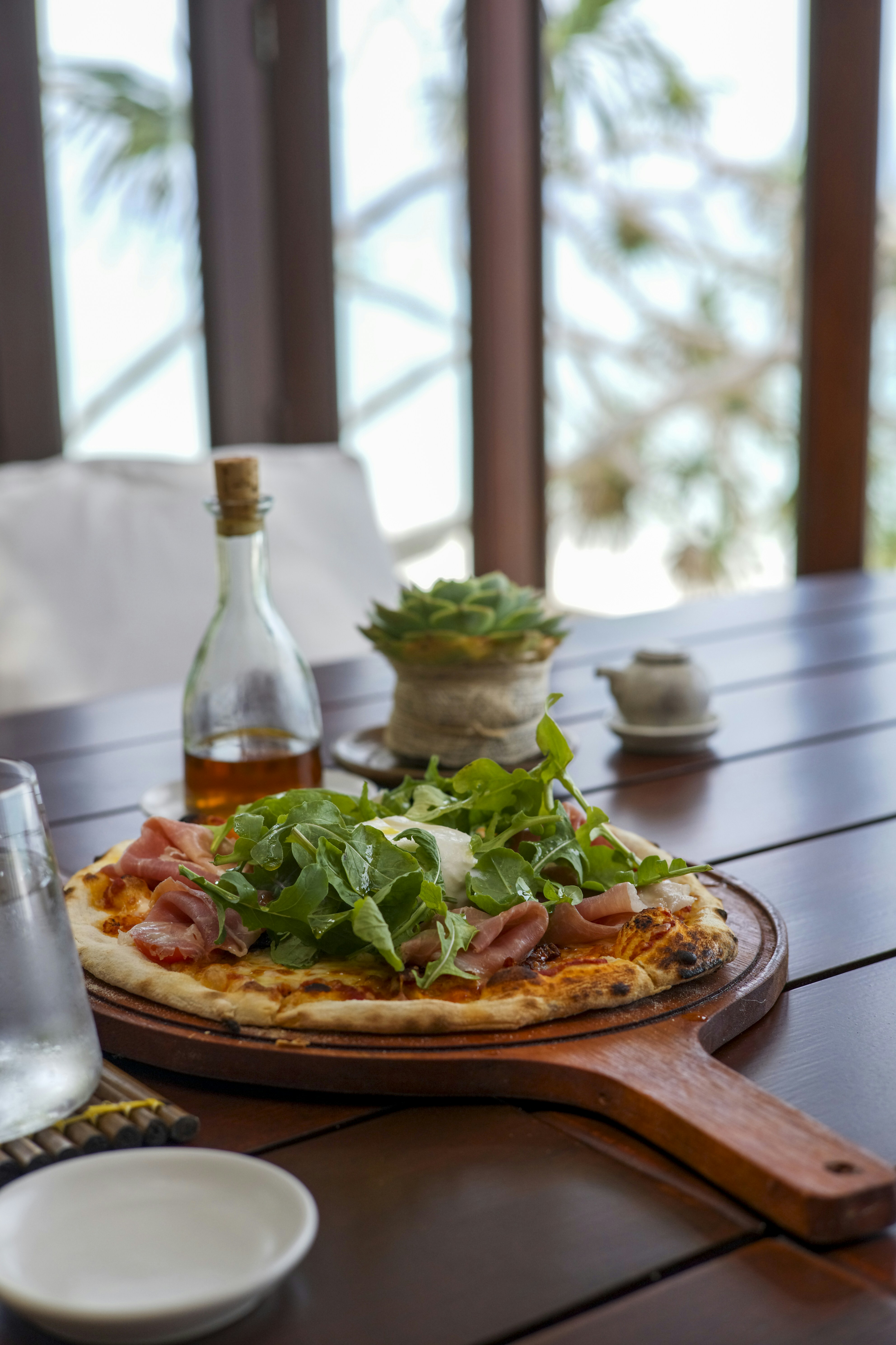 Sunlit Rustic Pizza on a Wooden Paddle: Prosciutto, Arugula and Fresh Greens