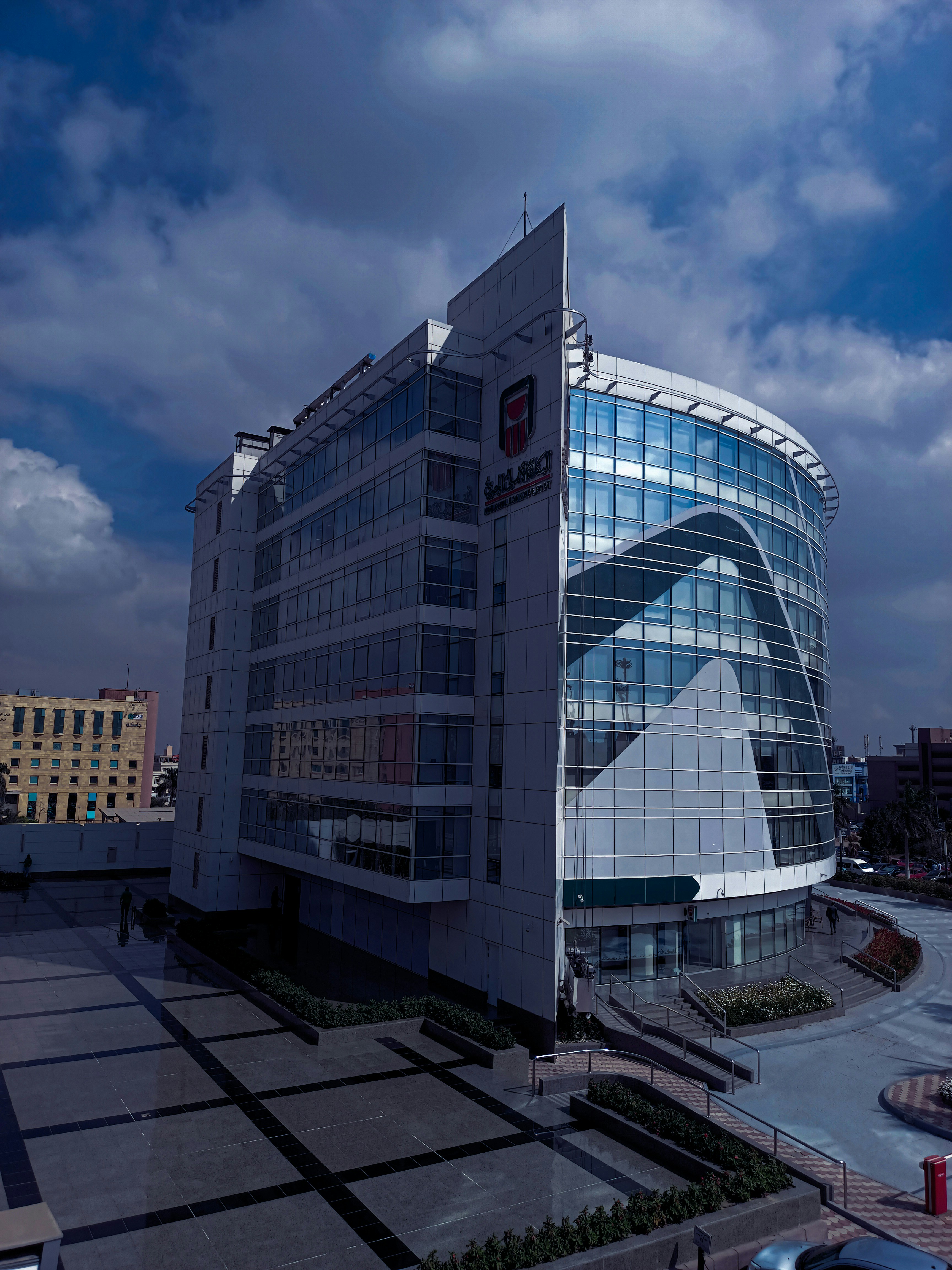 Contemporary office building with reflective glass facade and geometric design elements, set against a cloudy sky.