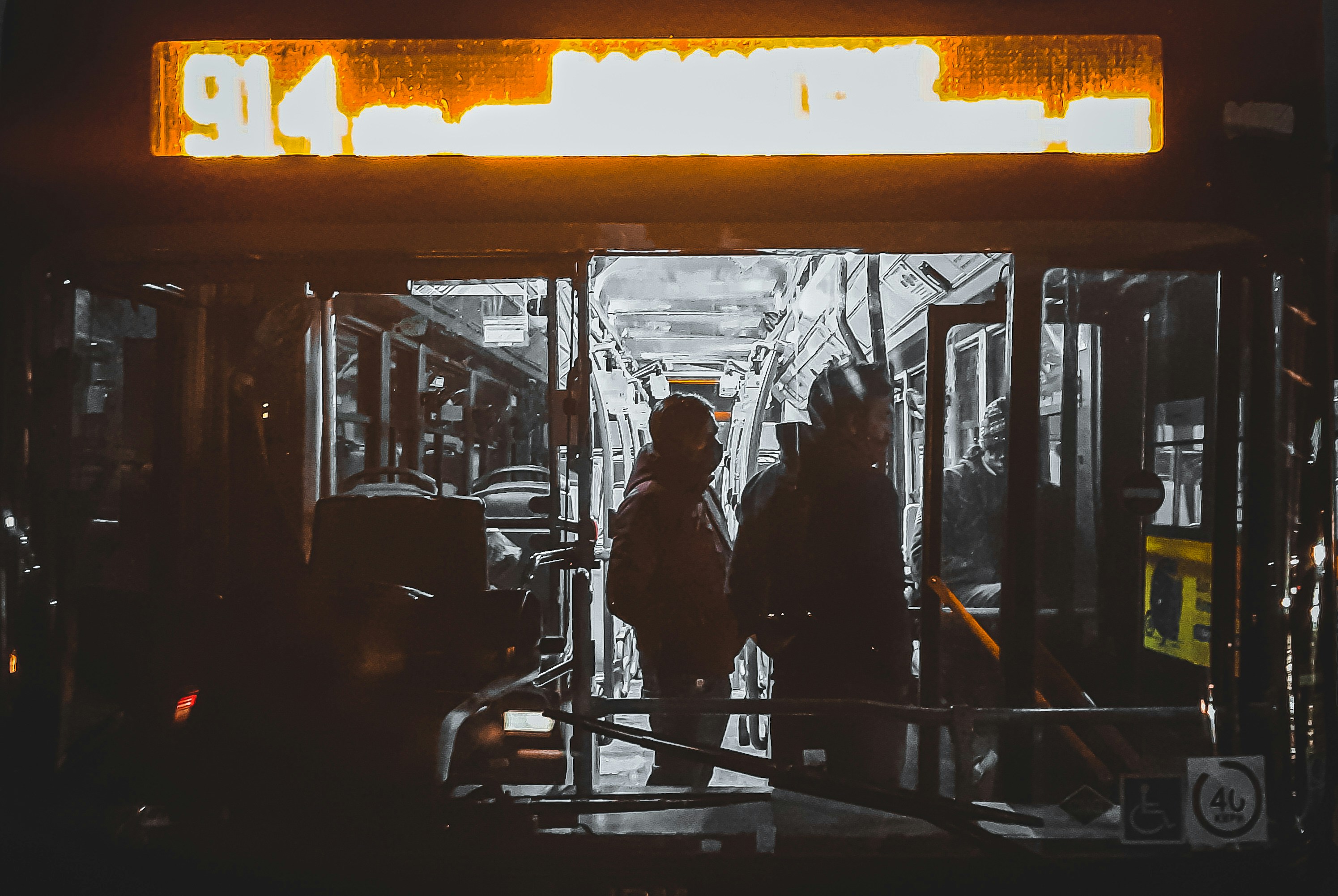 Silhouetted figures stand inside a bus, with illuminated route numbers glowing above. The scene captures the essence of urban commuting.