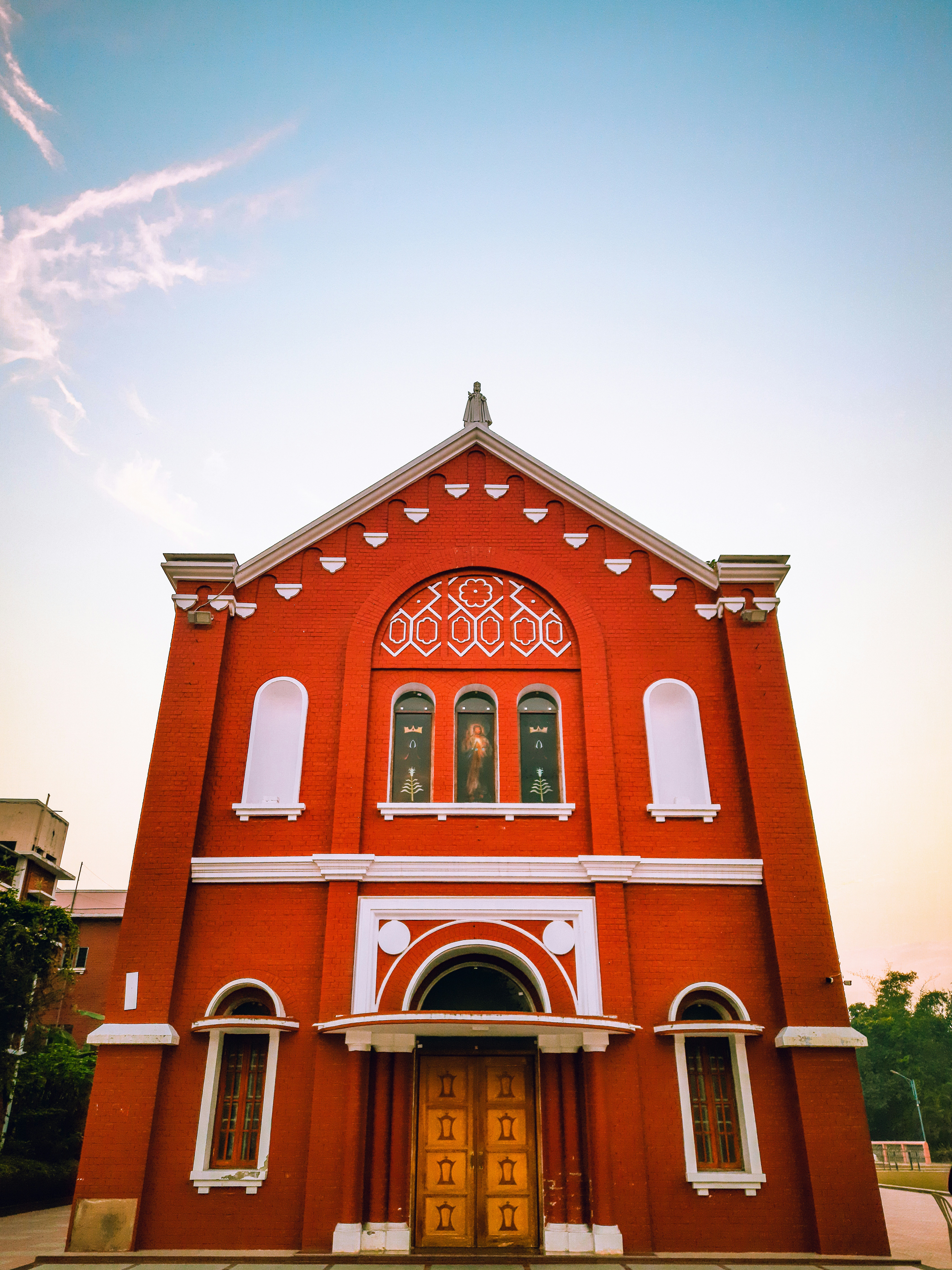 Historic red church with intricate designs and large wooden doors, framed by a soft evening sky.