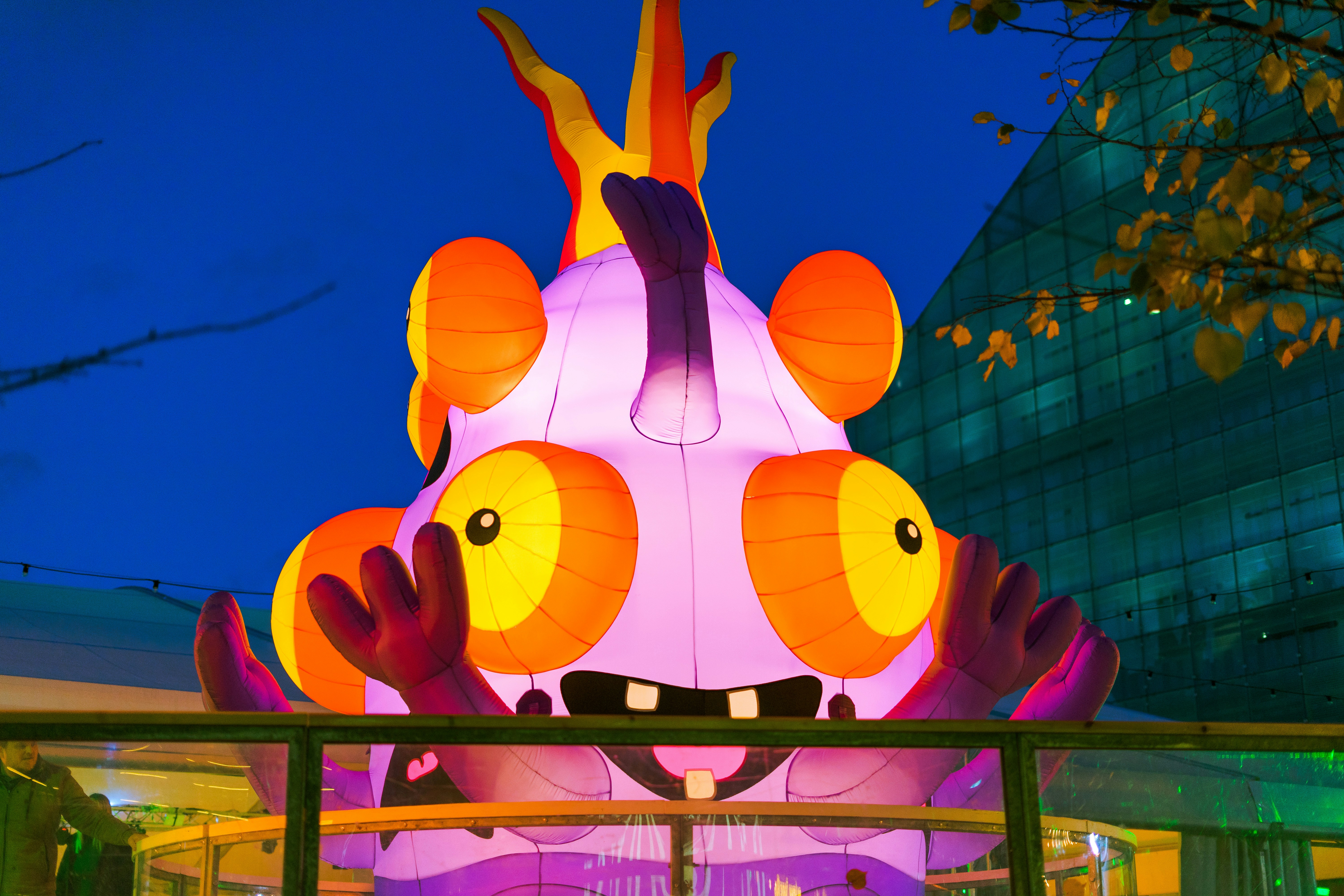 Glowing festival creature: a neon-lit mascot rising over railing at night