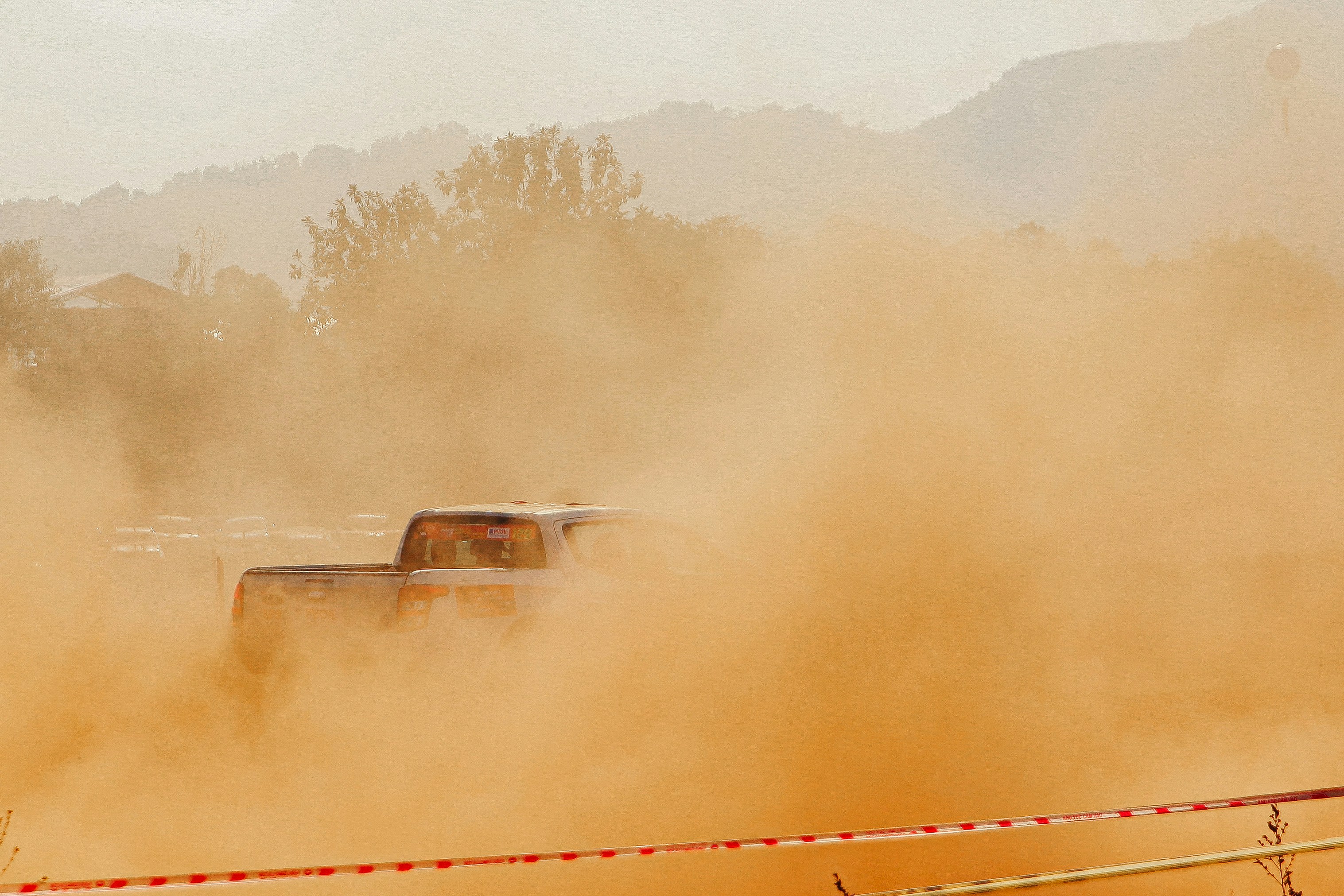 Dust Curtain: A Pickup Emerges Through an Orange Haze on a Rally Track